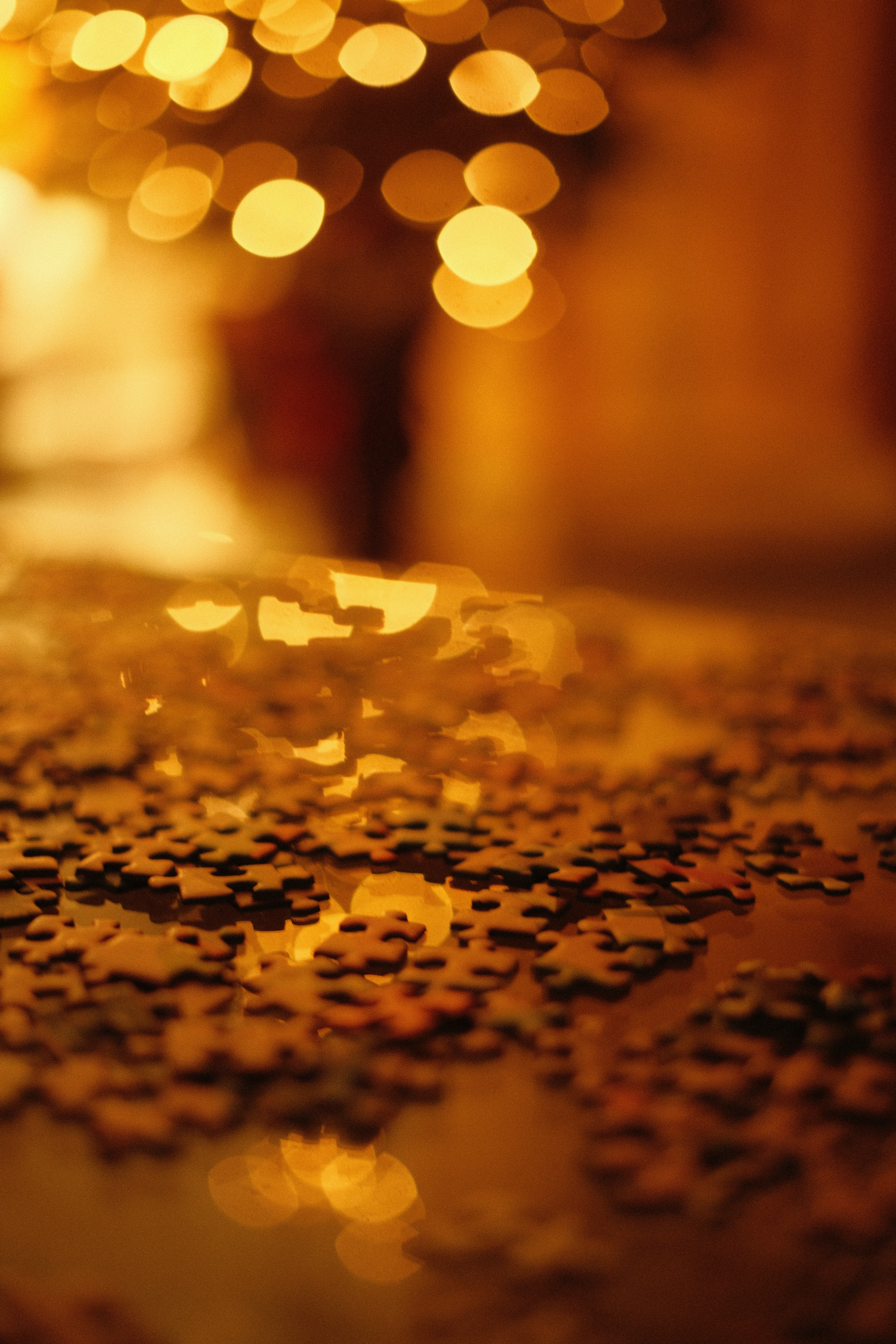 Scattered puzzle pieces on a reflective surface with bokeh lights.