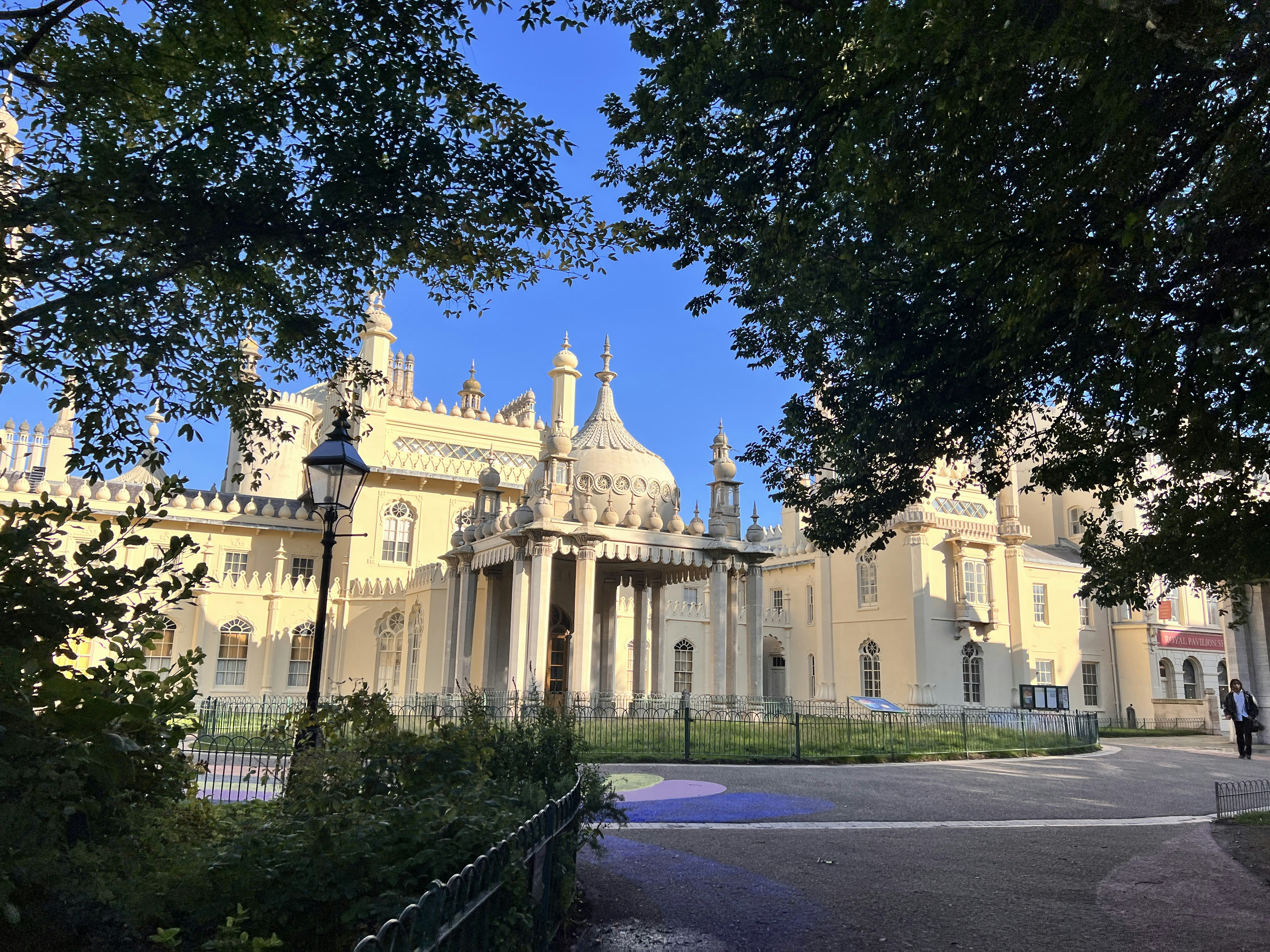 Ornate building with domes and spires surrounded by lush greenery and a clear blue sky.