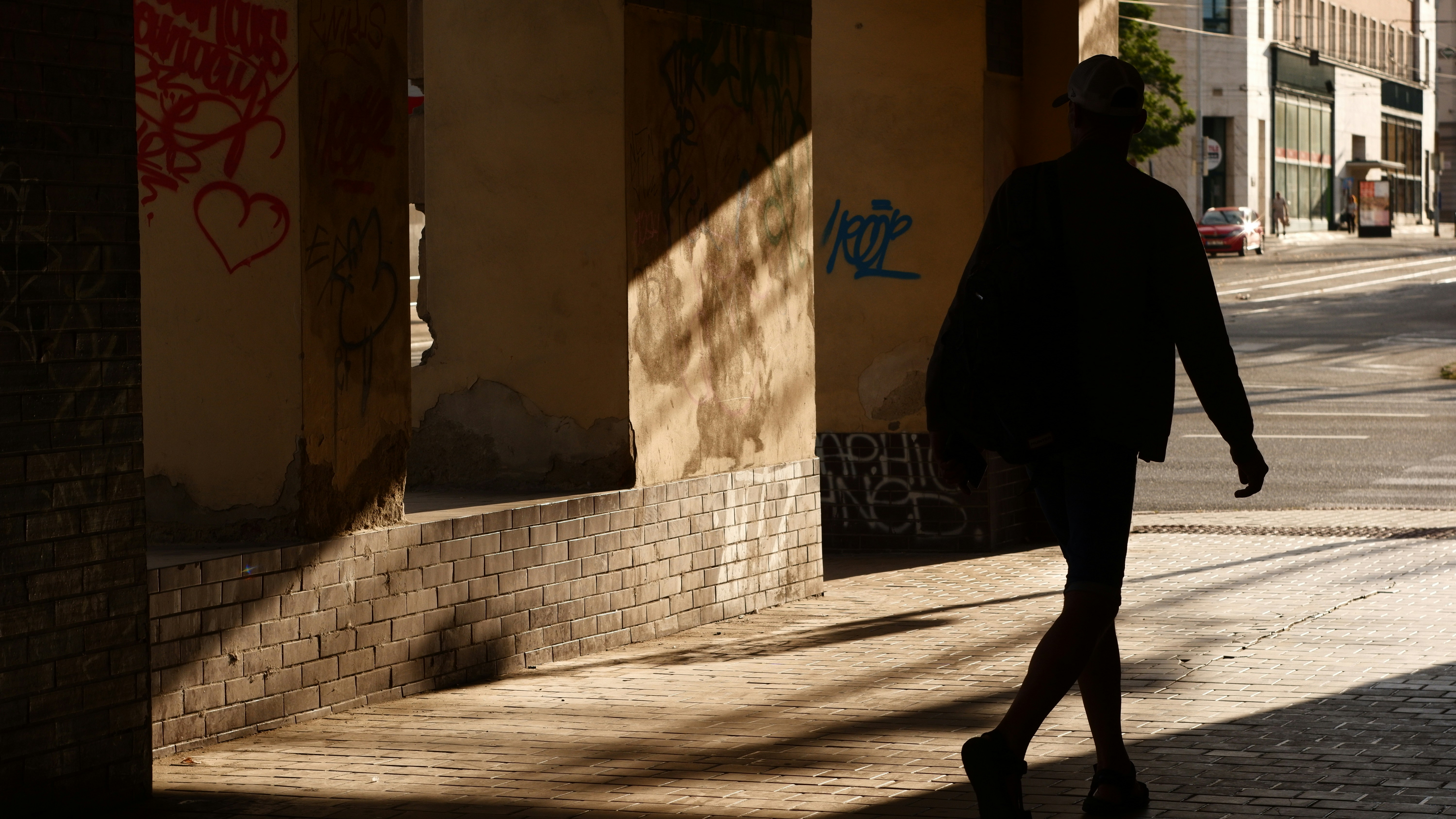 Silhouette of person walking on a sunny street.