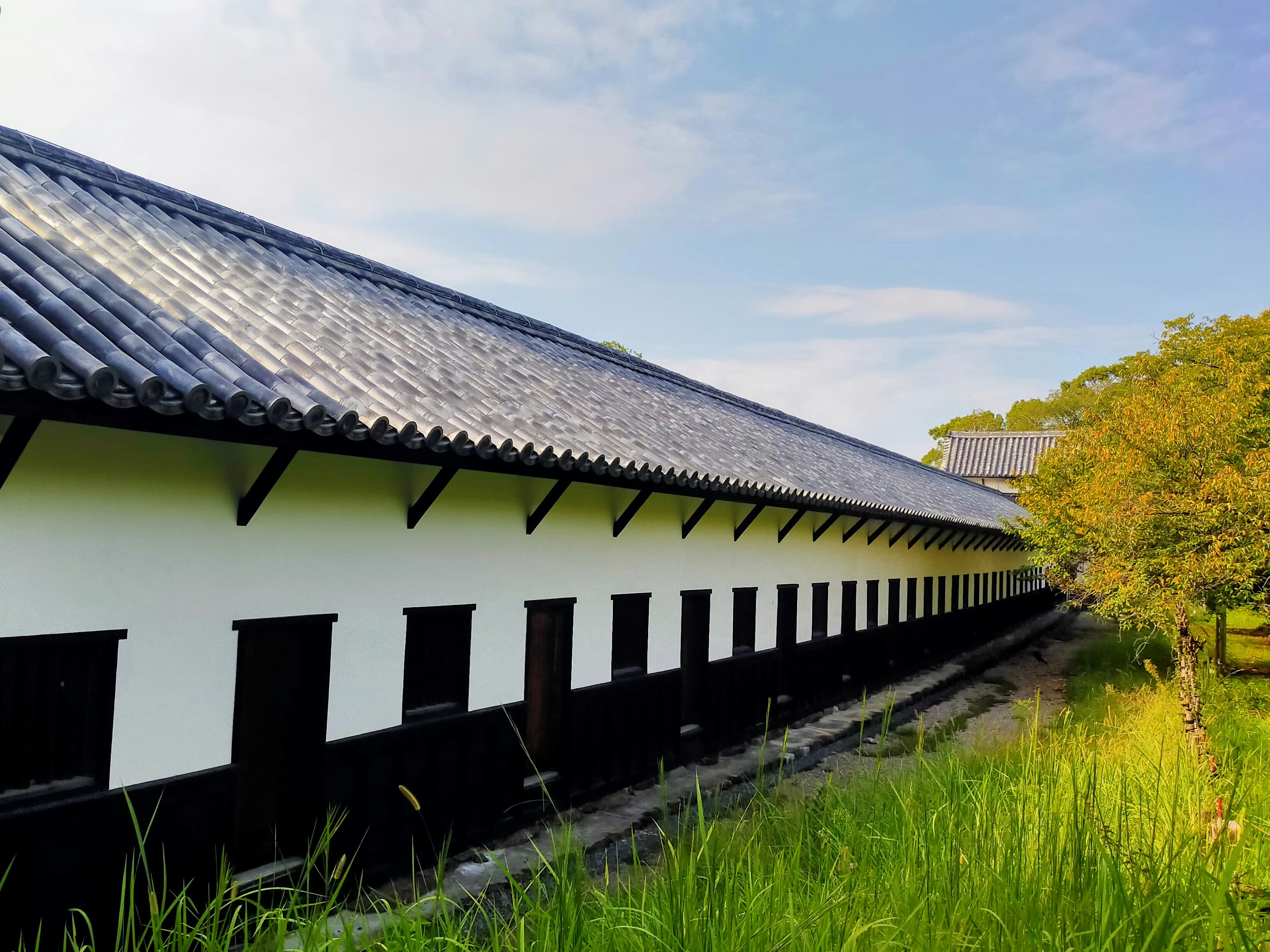 Long white building with black windows and tiled roof.