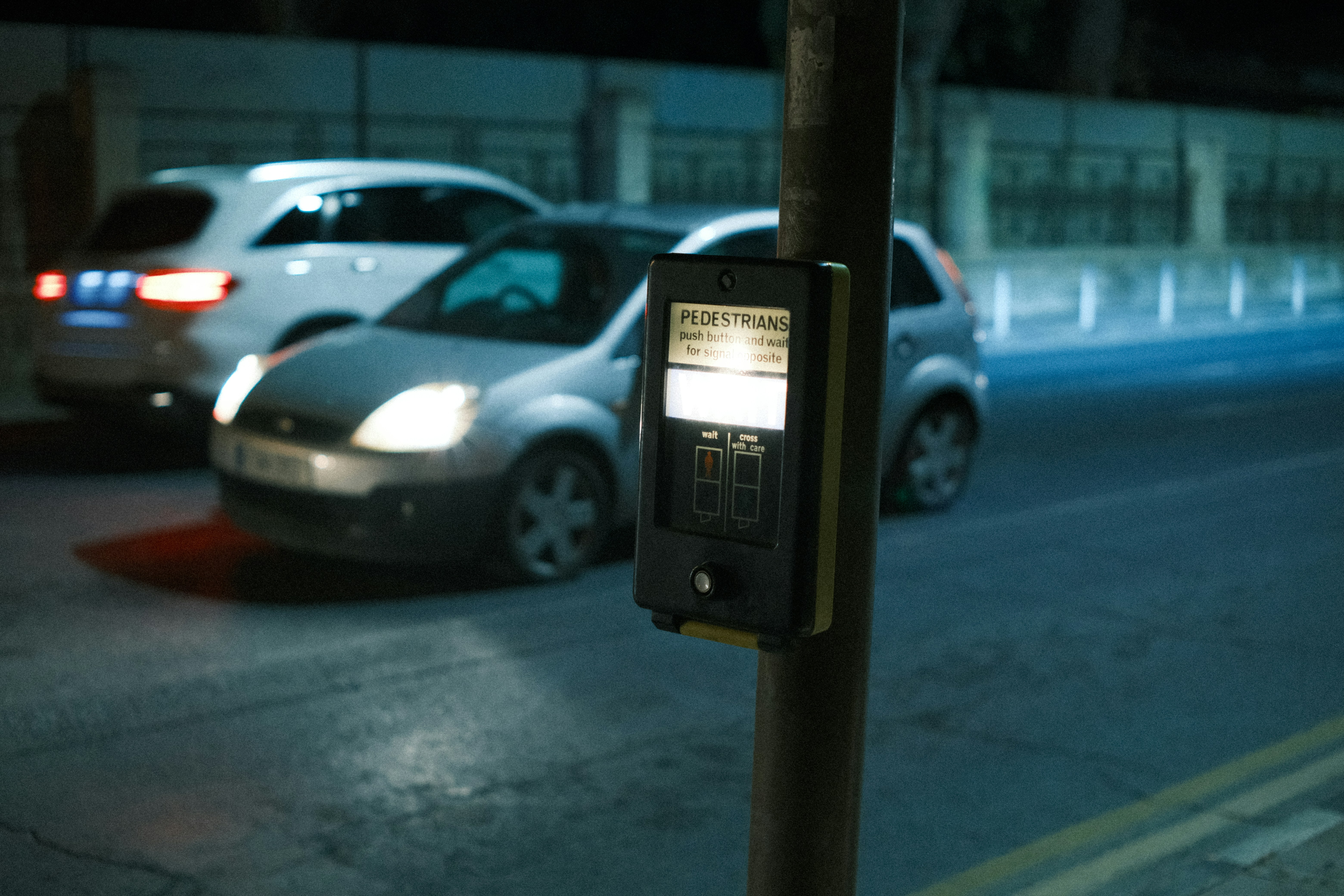 Cars driving at night near a pedestrian crossing button.