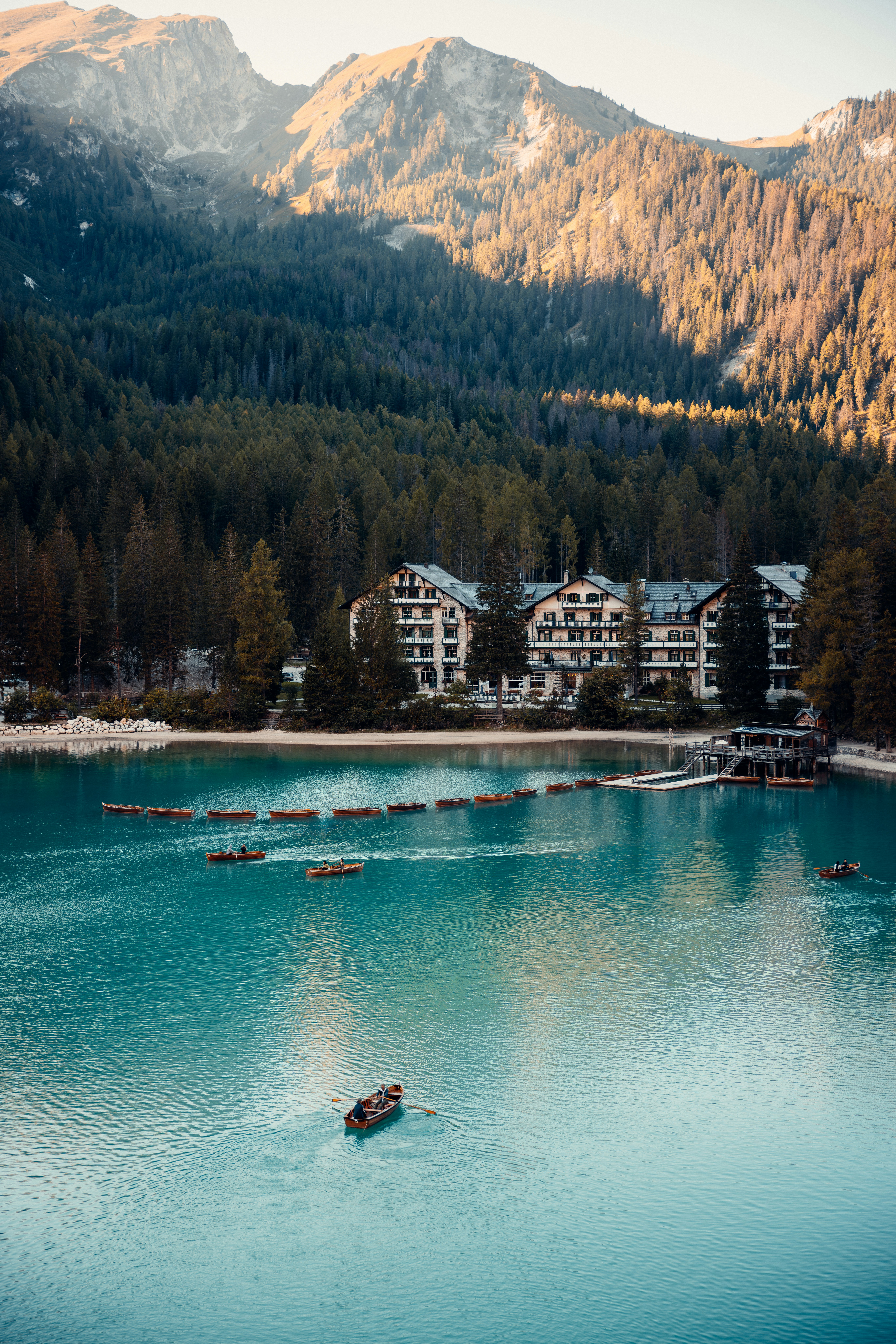 Lago Di Braise, Dolomiti | Boats on a turquoise lake with mountains and hotel.