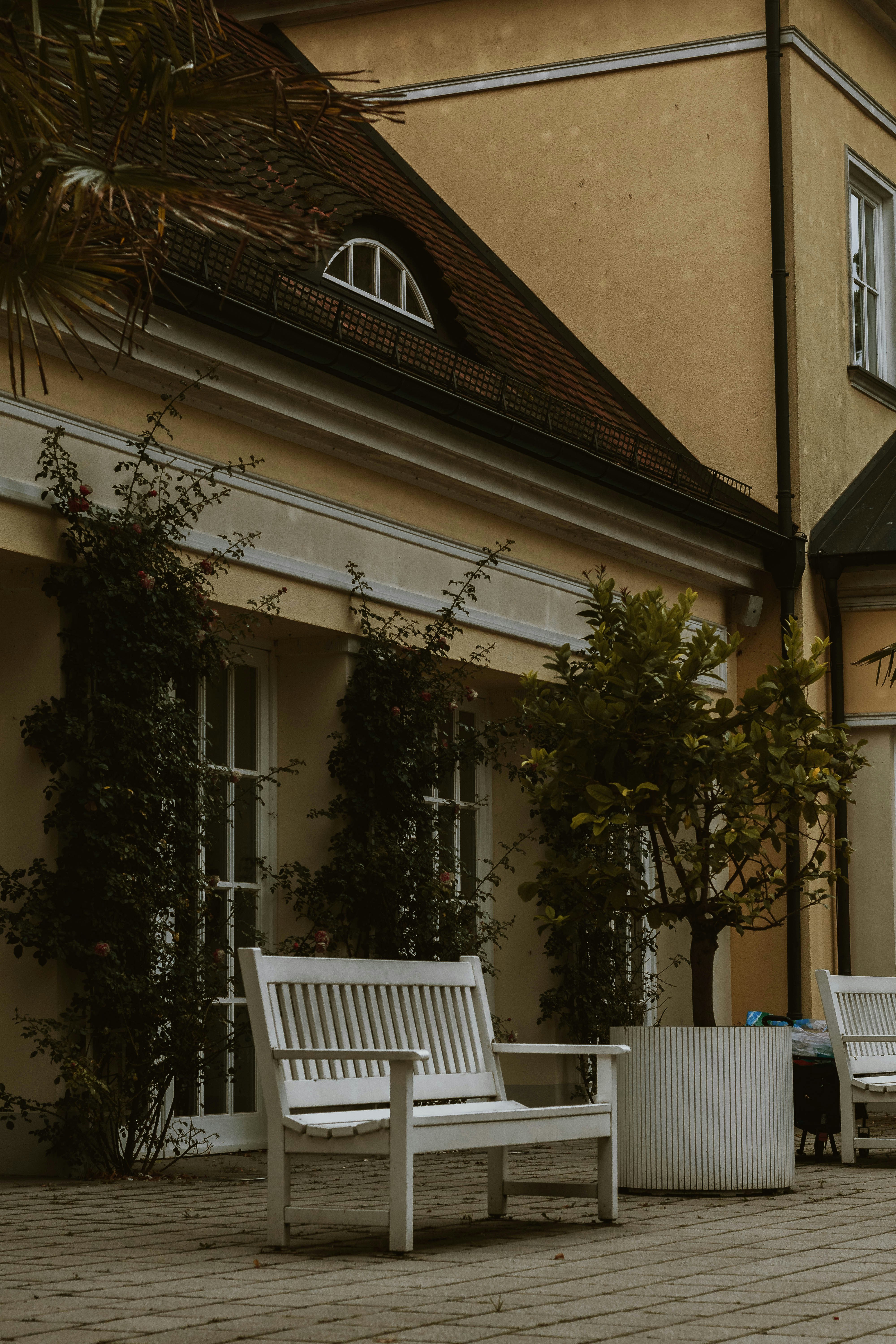 White park bench in front of a yellow building.