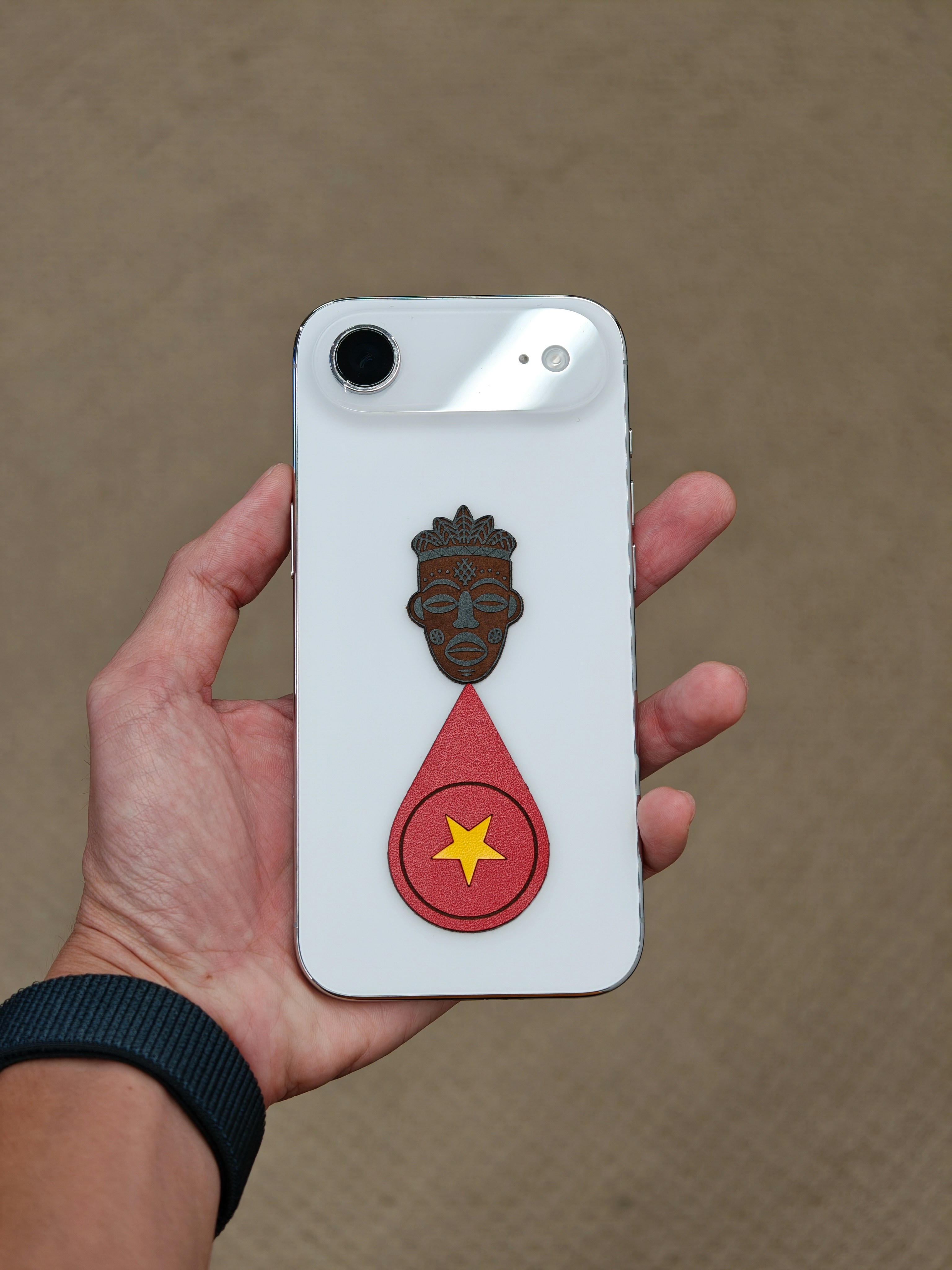 iPhone Air Cloud White with leather sticker by khacten.com | Hand holding white phone with tribal mask sticker.