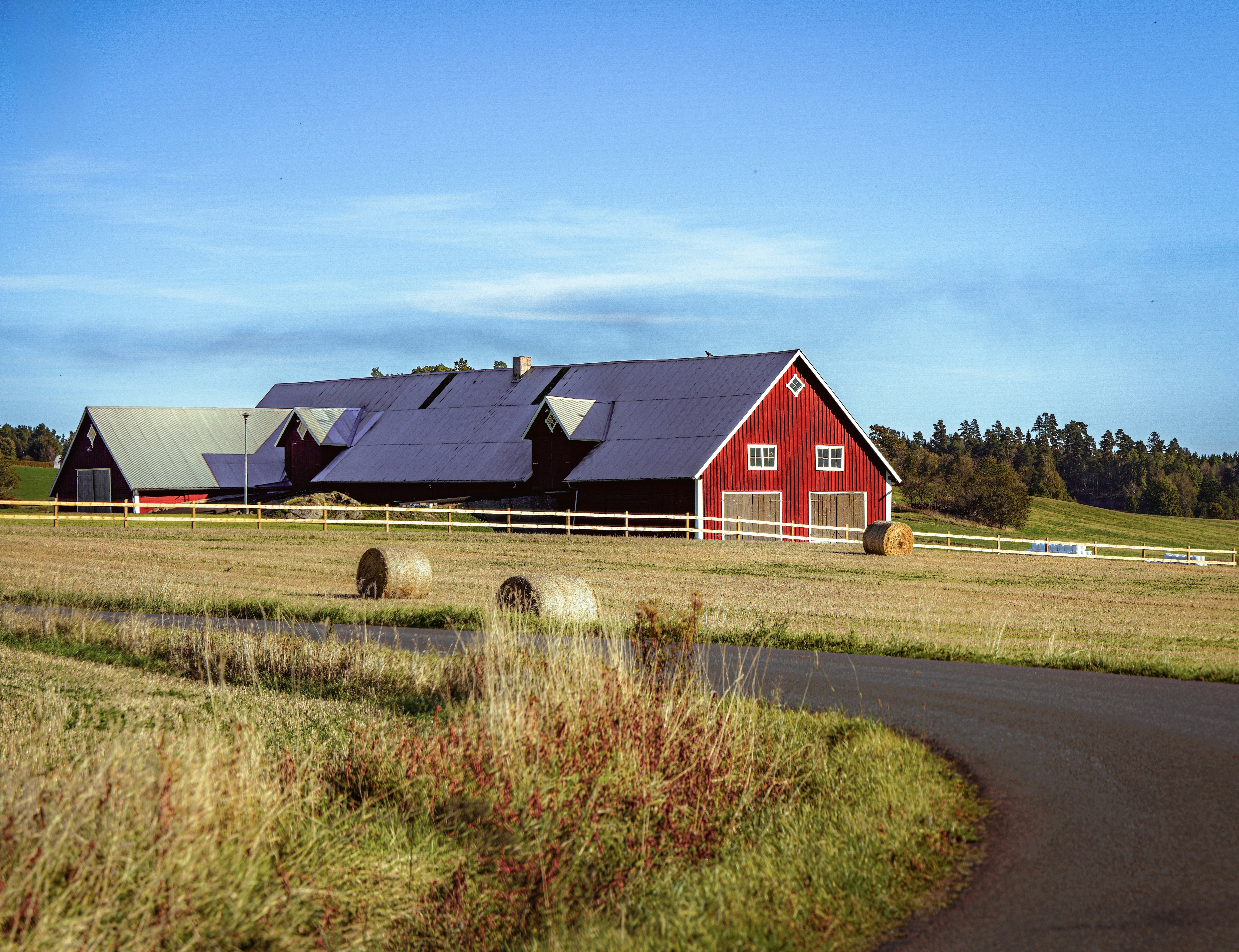Red barn with hay bales in a field.