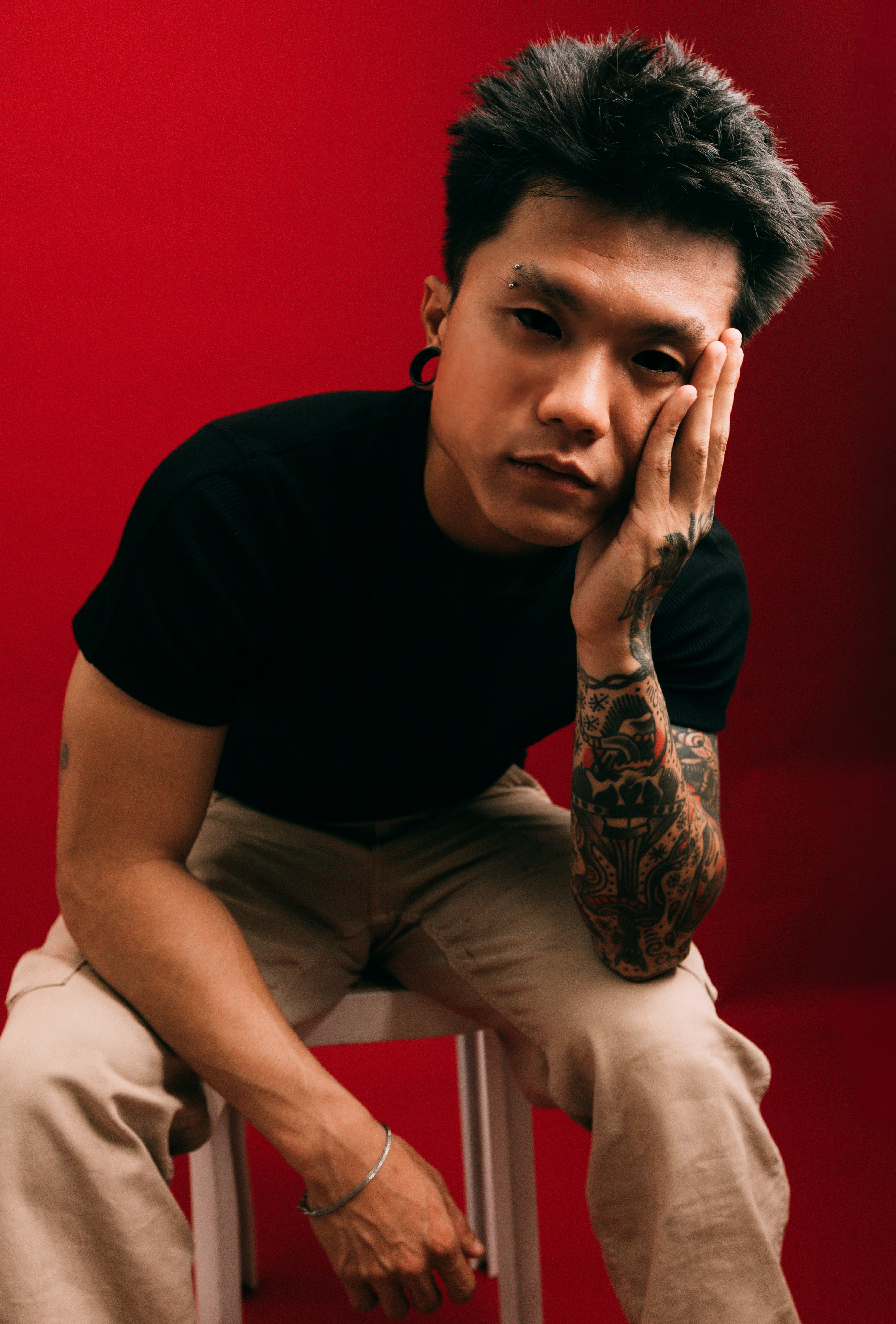Young man with tattoos rests head on hand.