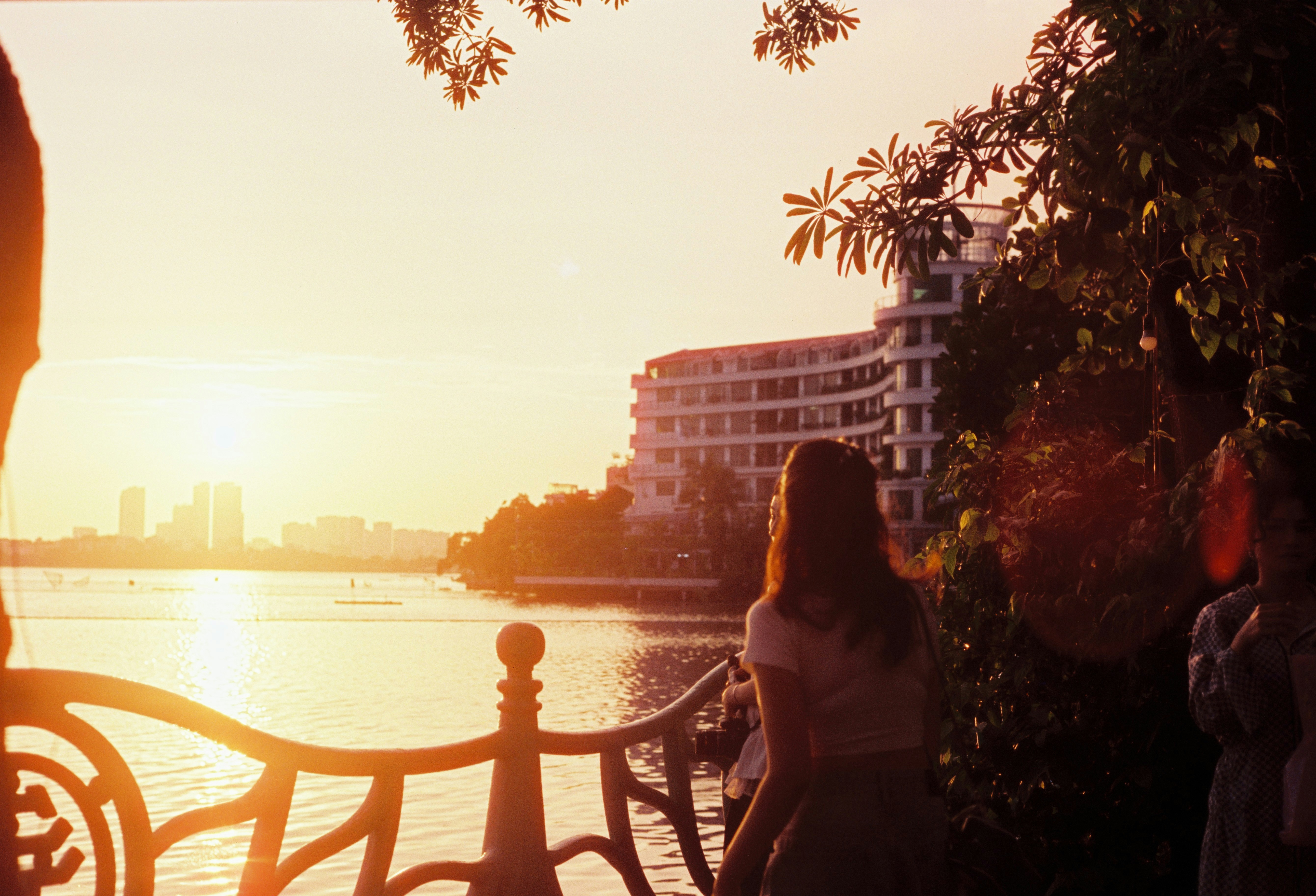 People watch sunset over a tranquil lake with city skyline.