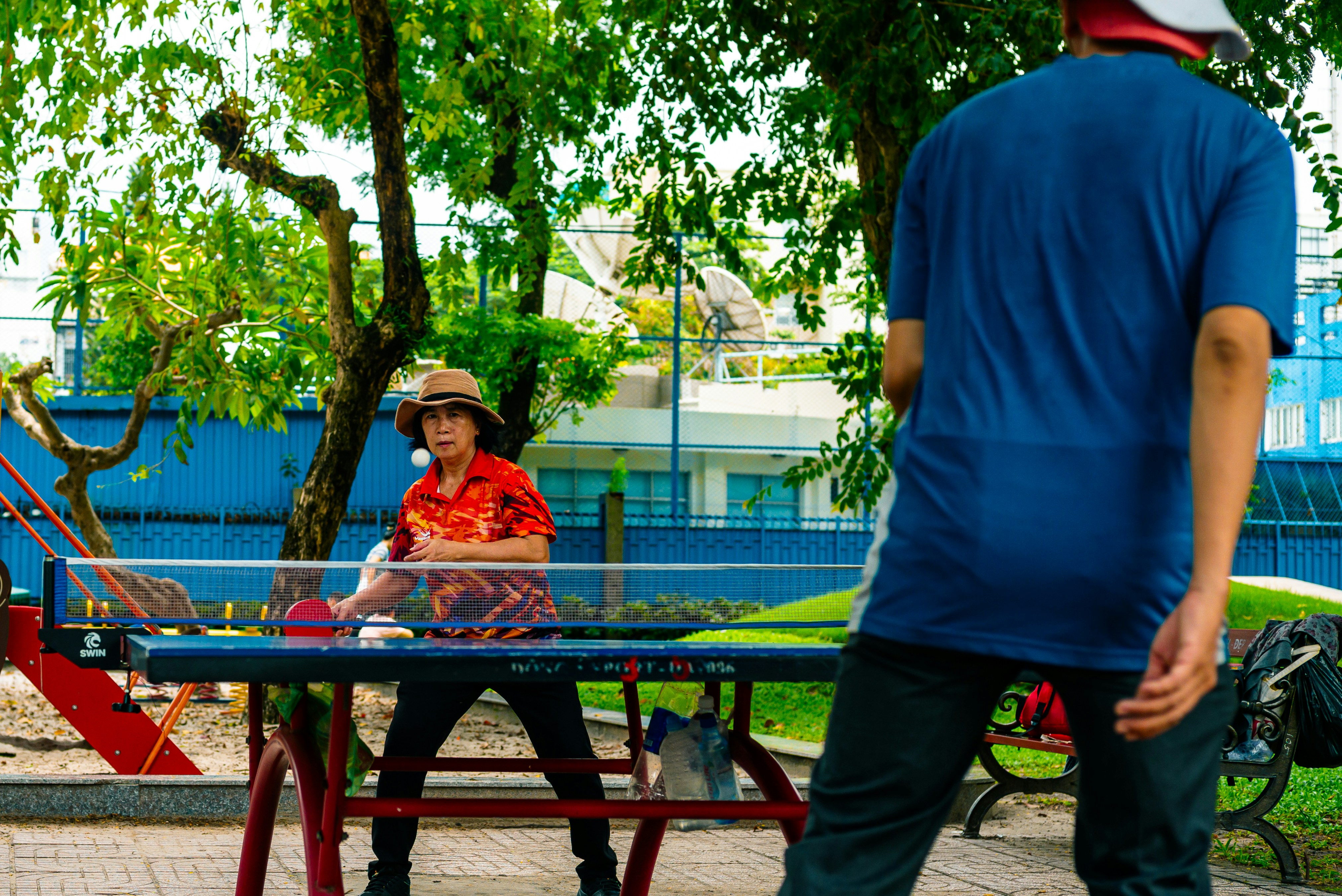 Two players engaged in a lively game of table tennis, surrounded by lush greenery in a vibrant park setting.