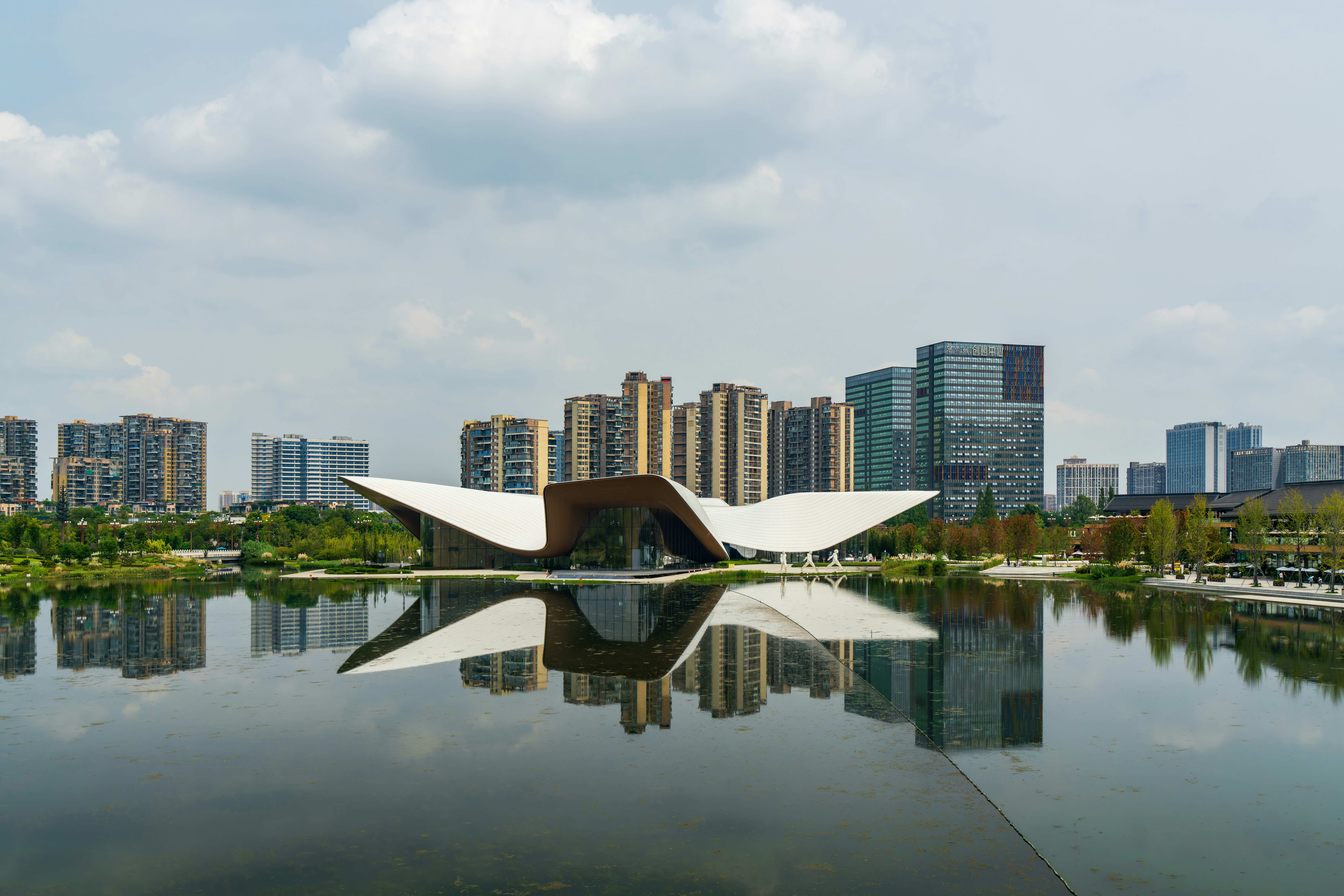 Chengdu Art Museum | Modern building reflected in a calm lake with city skyline.