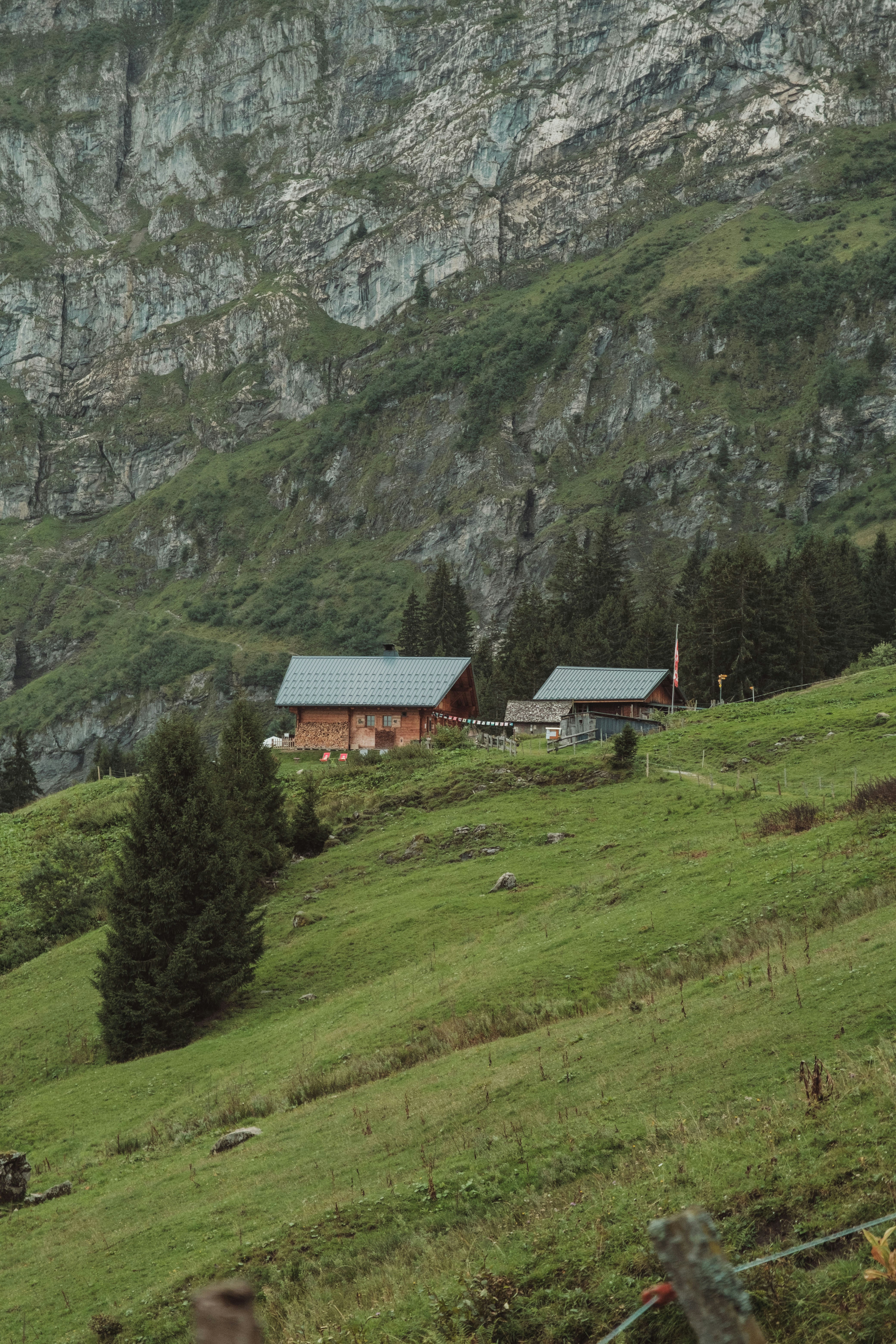A traditional Swiss mountain chalet nestled in the forest of Champéry, Switzerland. | Wooden cabins nestled on a grassy mountain slope.