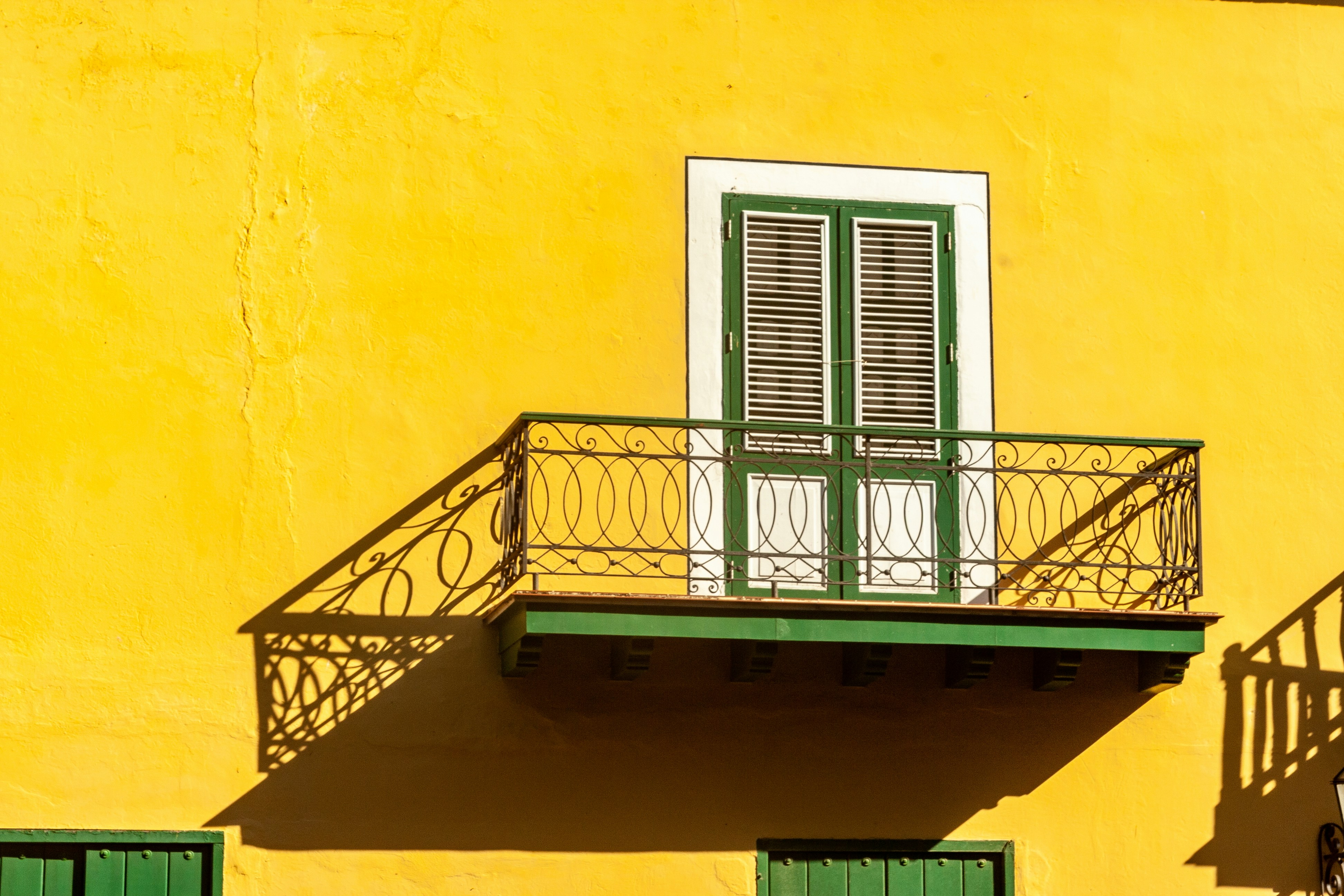 Yellow Wall | A green balcony casts a shadow on a yellow wall.