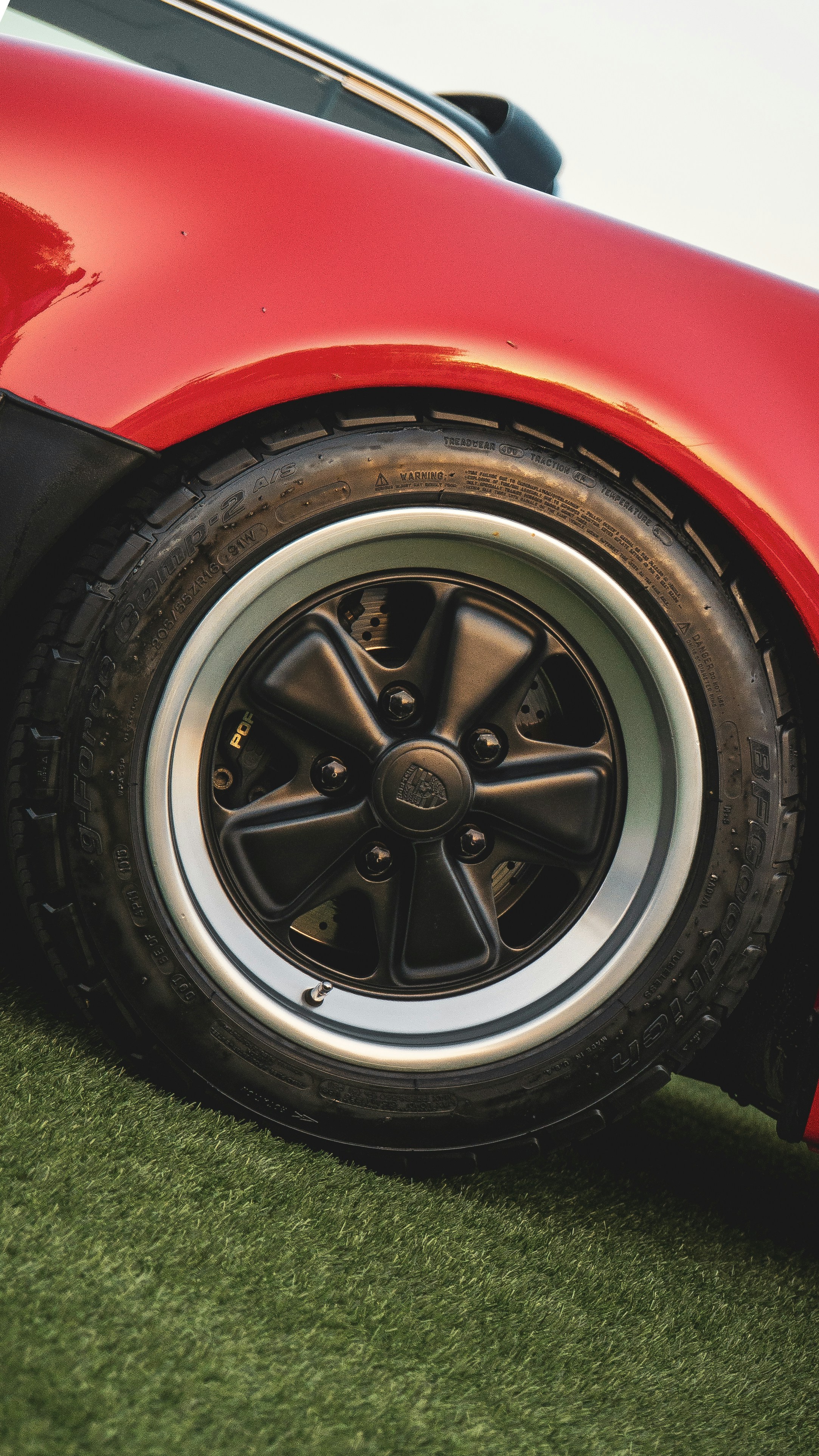 Close-up of a classic car's wheel, showcasing its intricate design and glossy finish against a green backdrop.