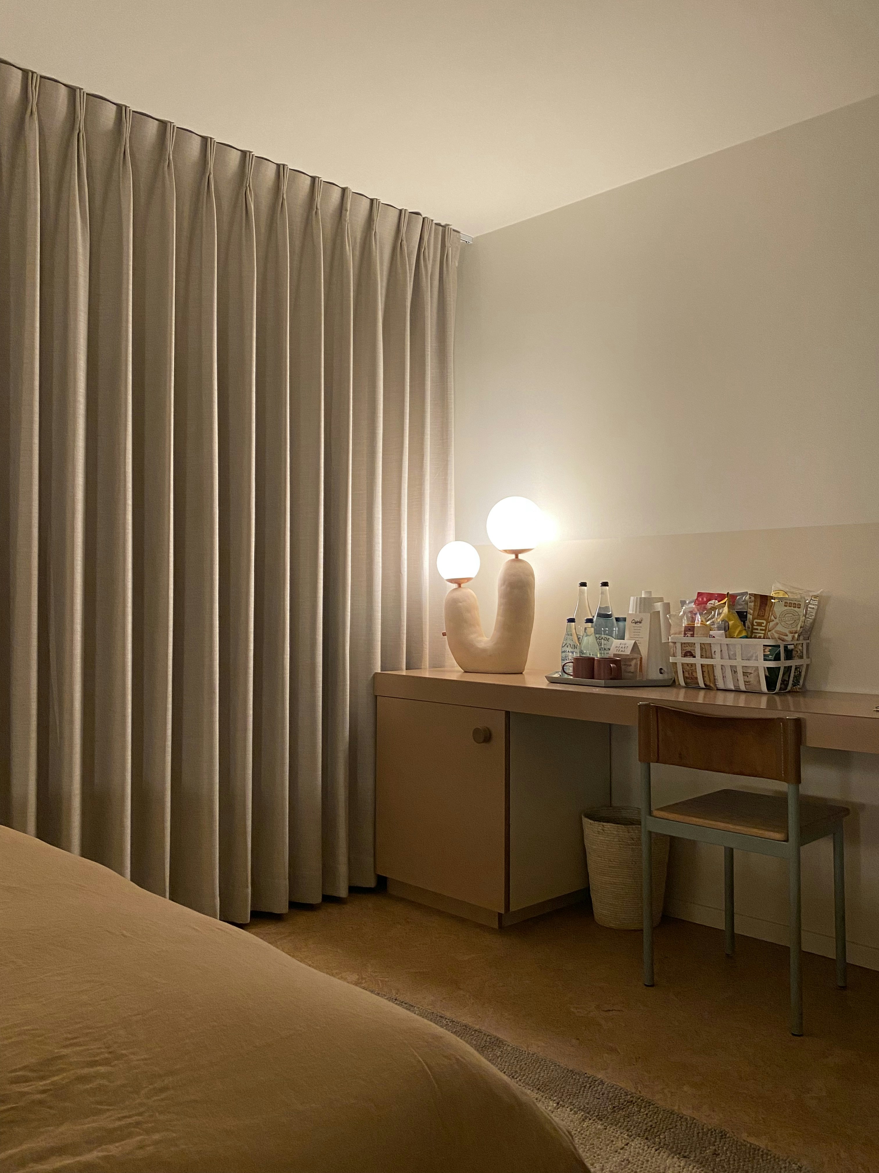 Hotel room desk with snacks, drinks, and lamp.