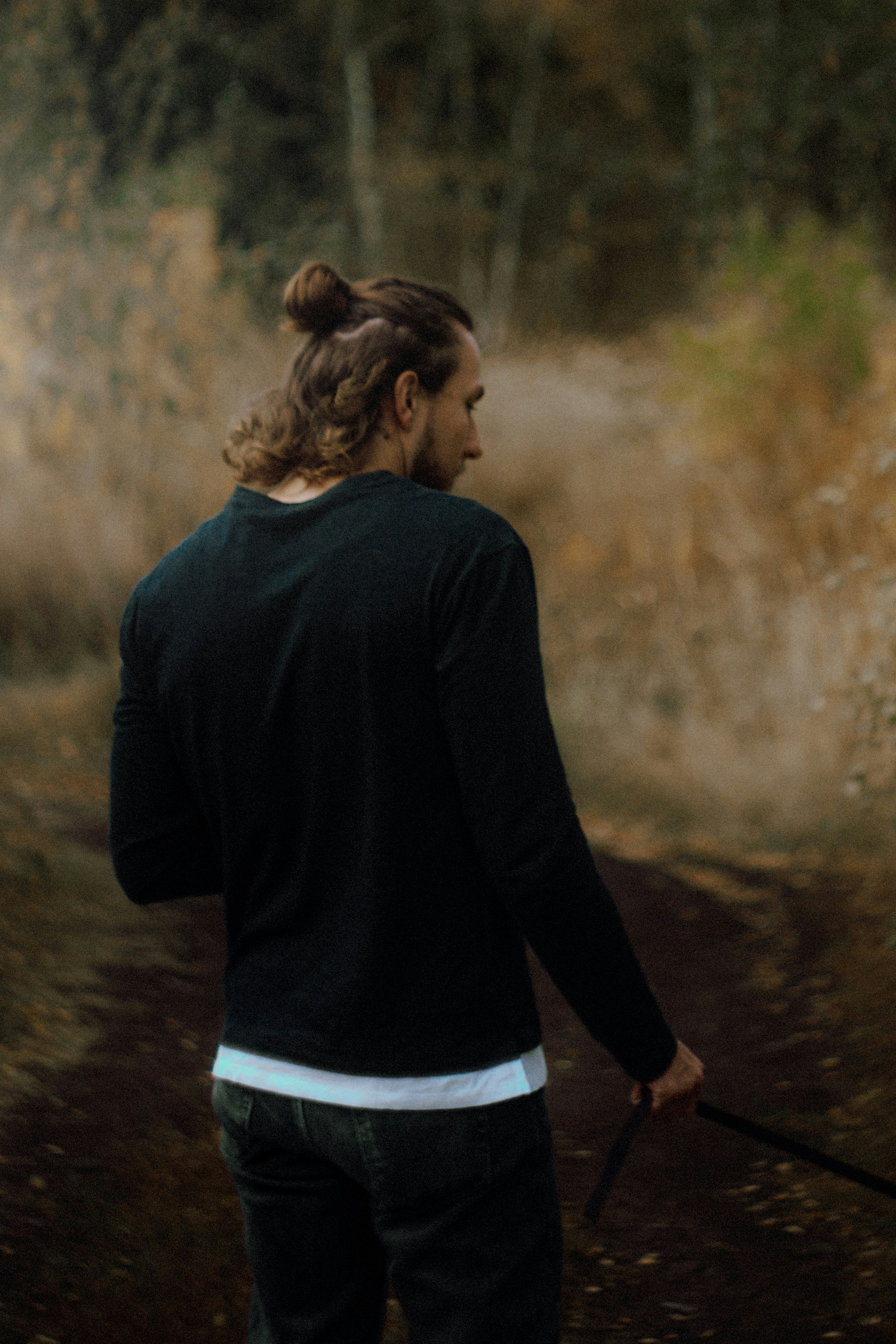 Man with bun walking on dirt path in autumn