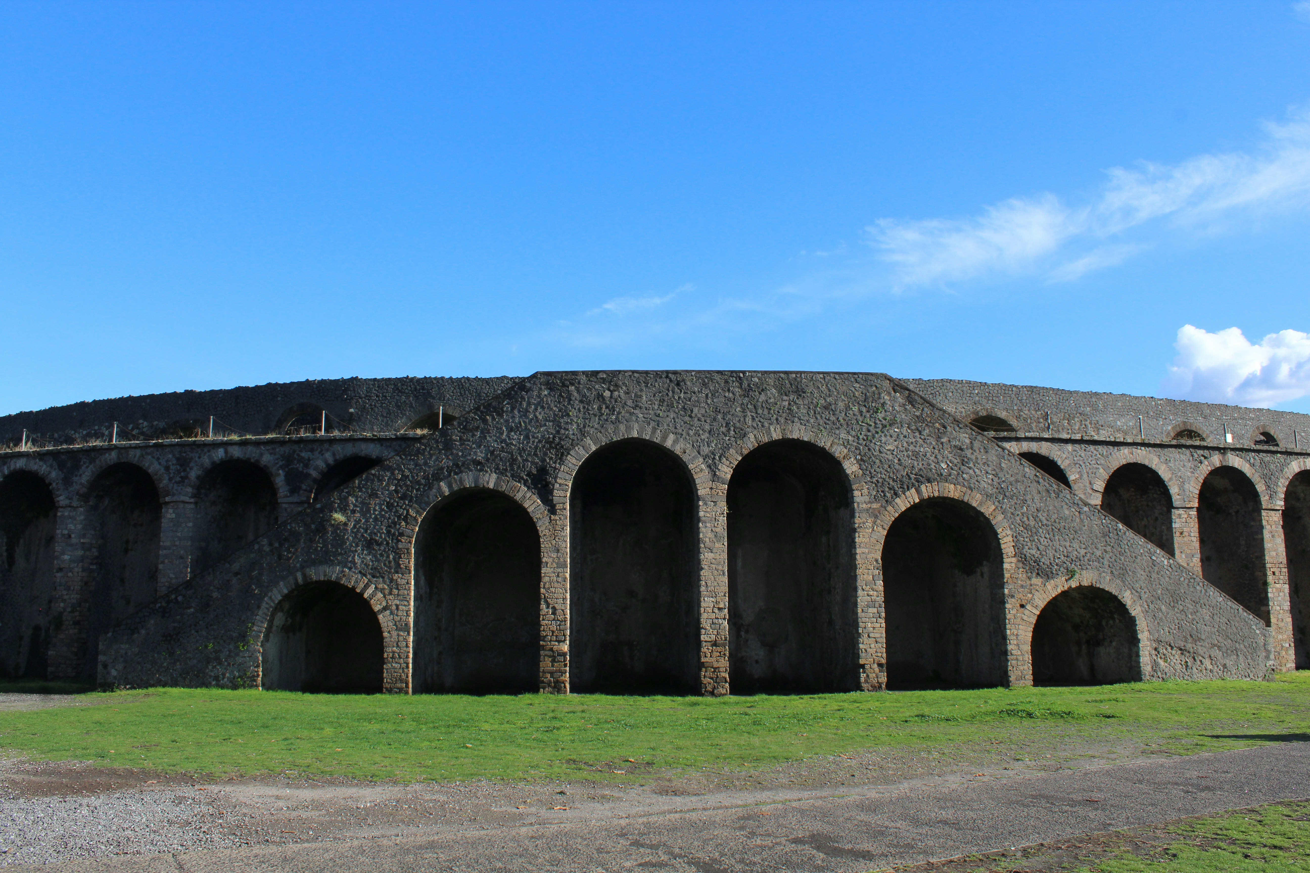 Pompeya/Pompeii ancient Roman city buried by the eruption of Vesuvius in 79 AD | Ancient stone amphitheater with arched walkways under blue sky