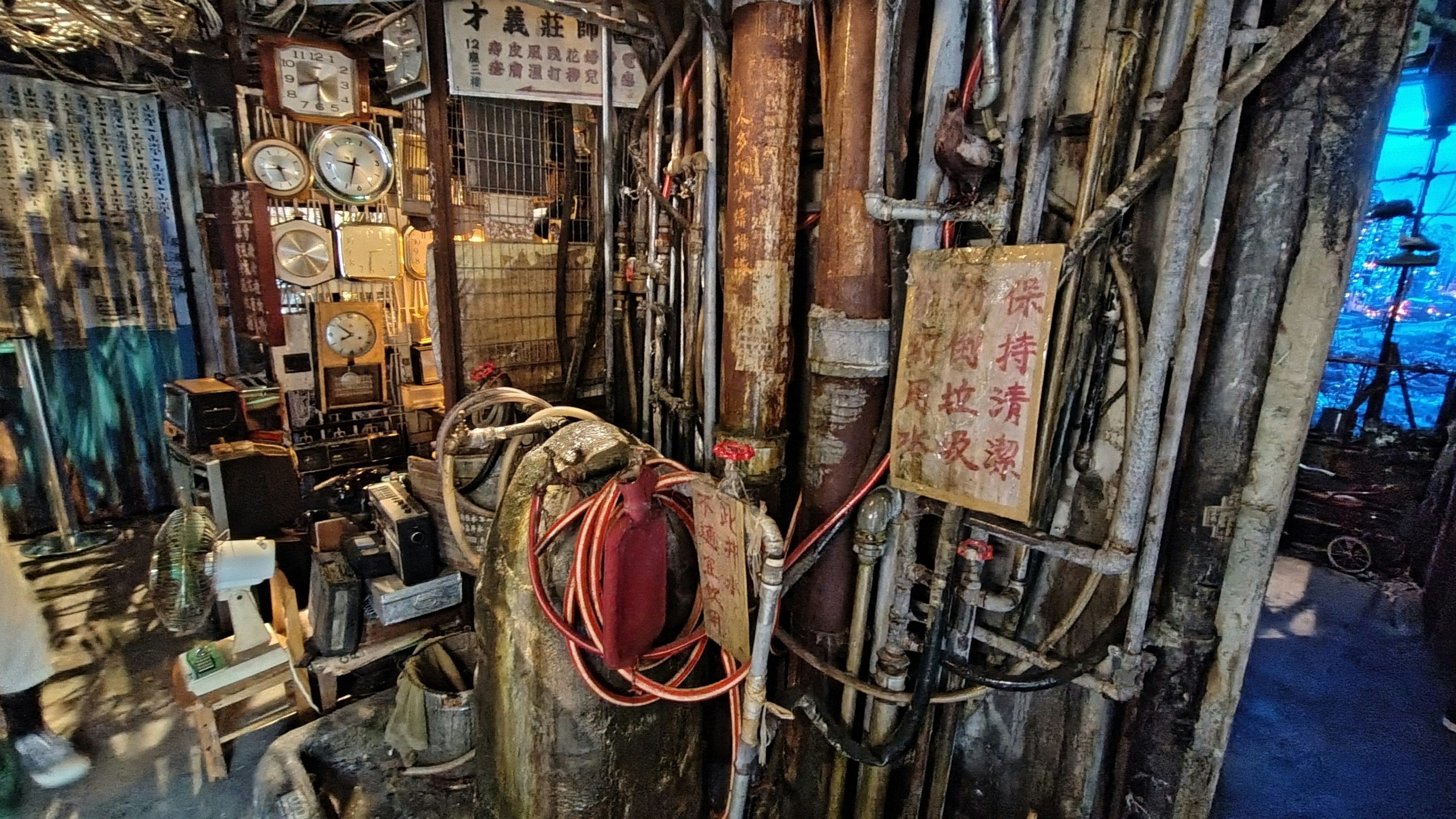 Recreation of how a shop was in Kowloon Walled City, Hong Kong | Cluttered room with pipes, wires, and signs.