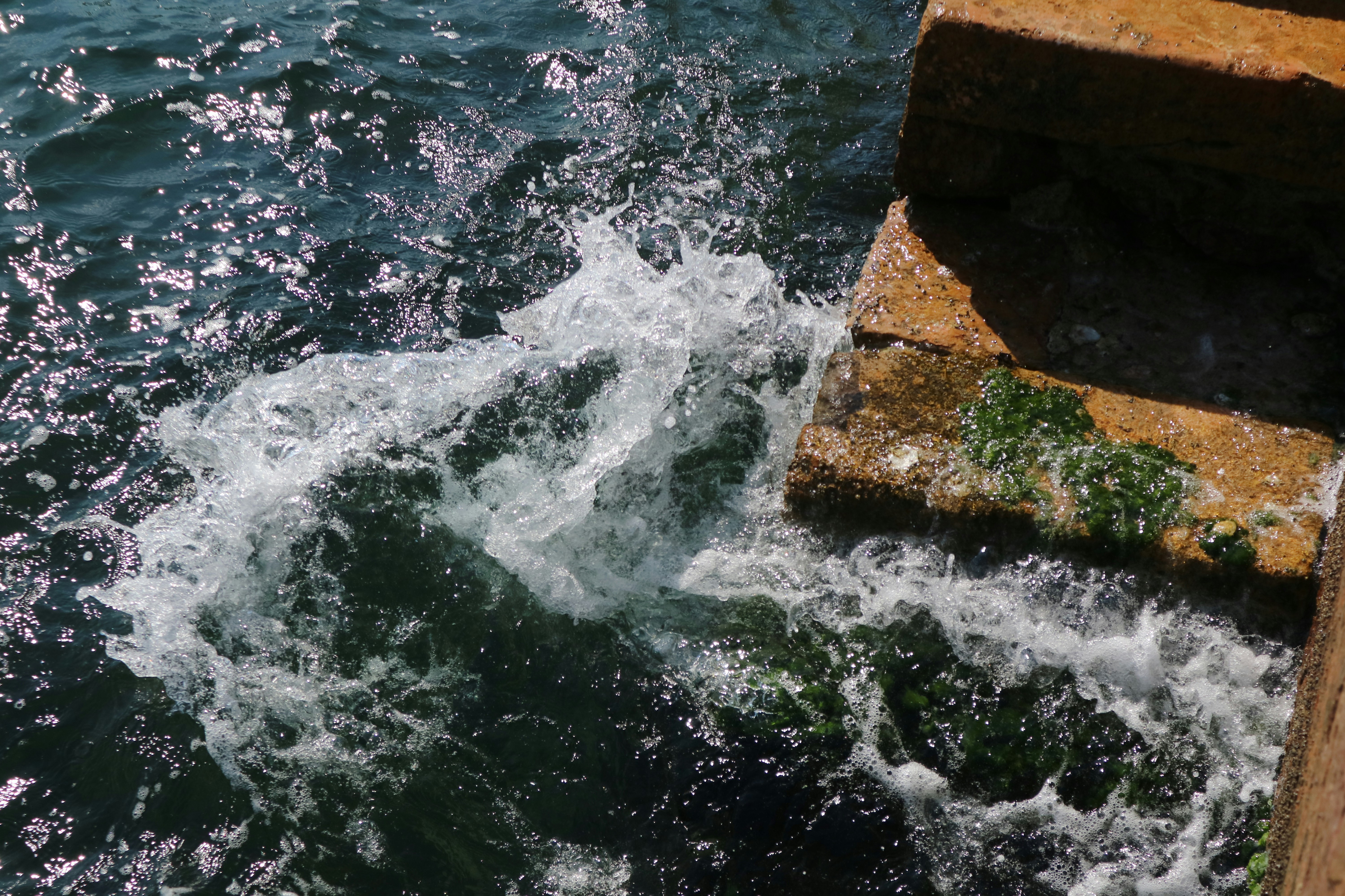Waves crashing against concrete steps with moss.
