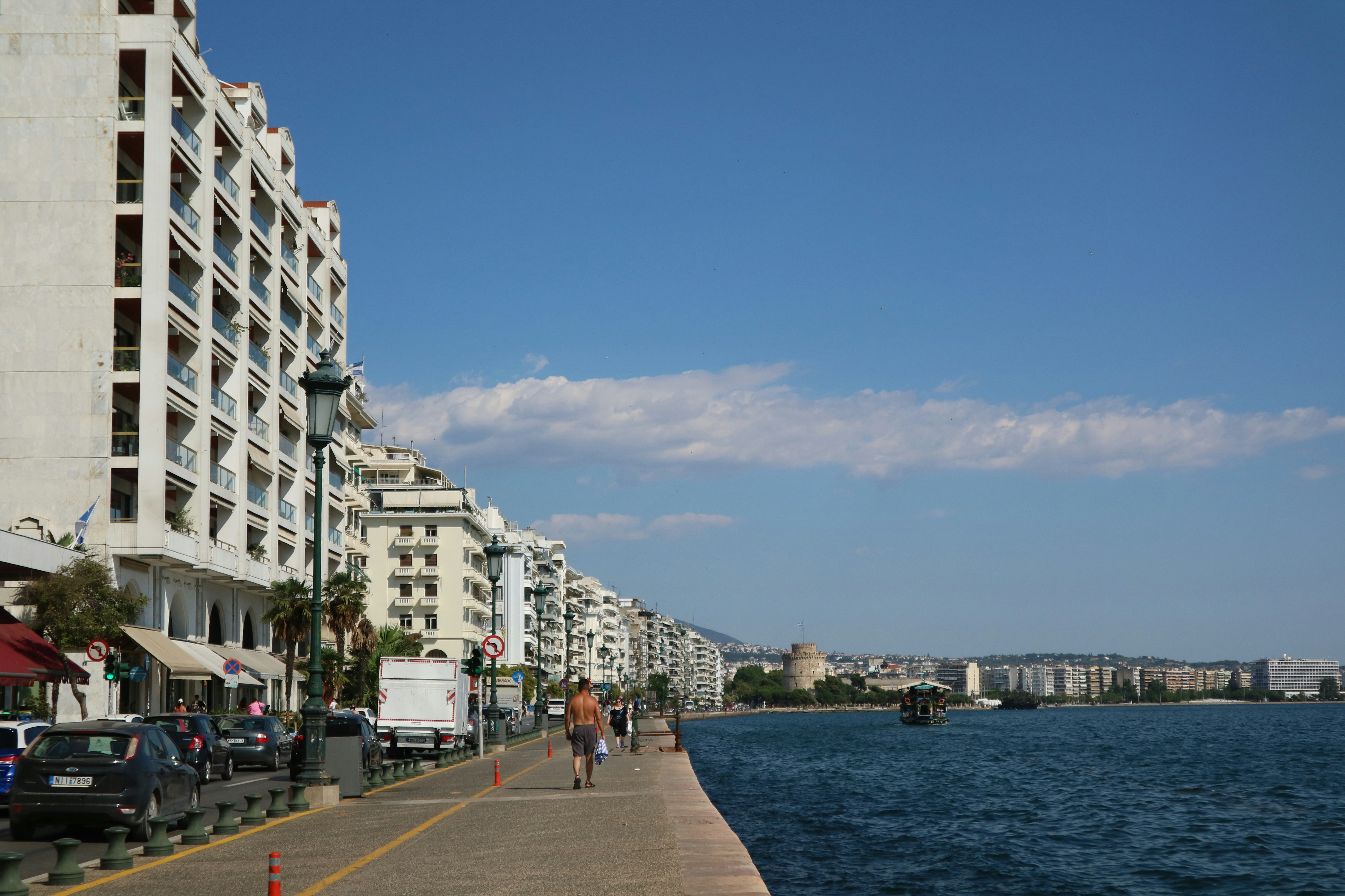 Buildings line a waterfront promenade with the sea.
