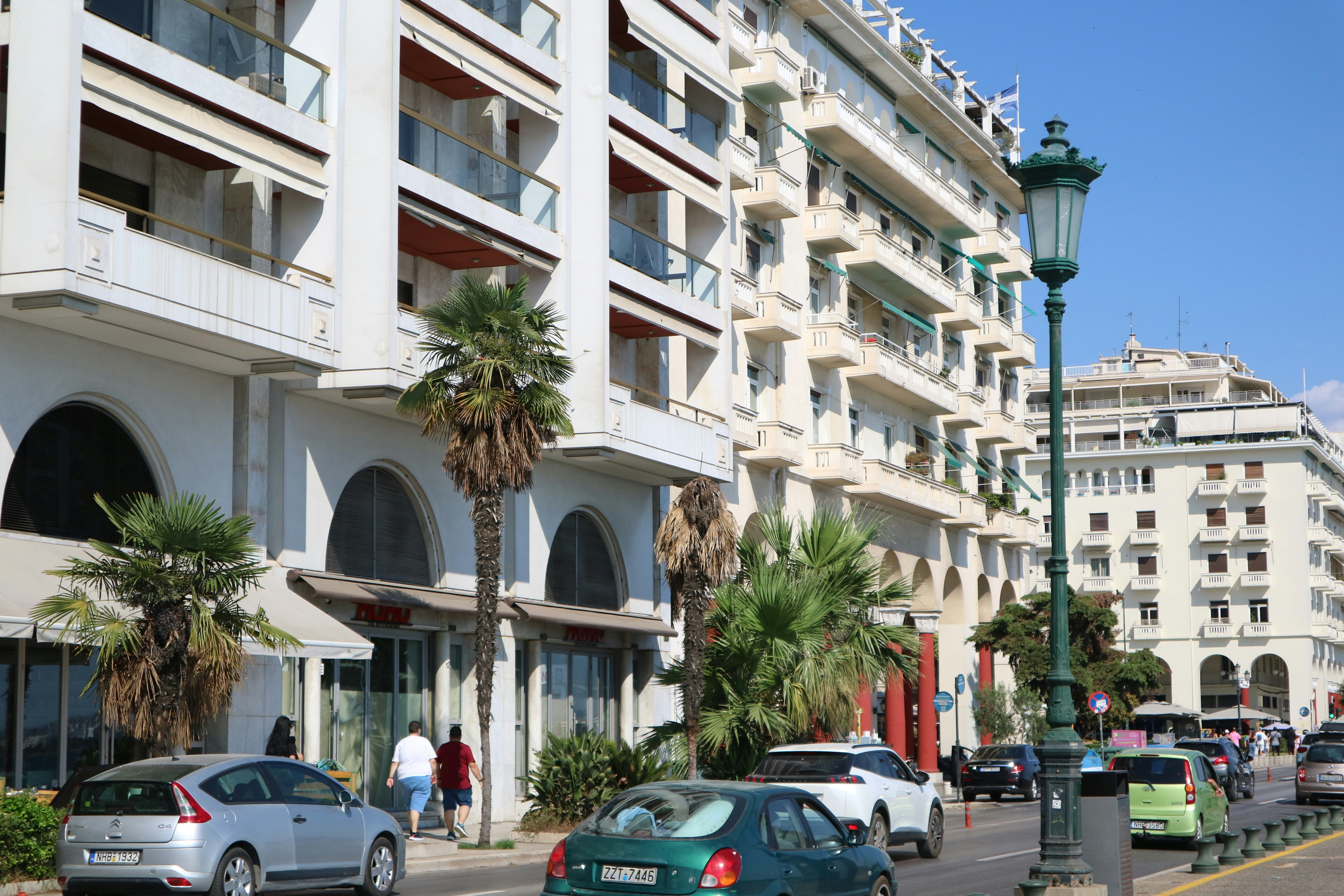 Vibrant street scene showcasing modern architecture alongside palm trees and parked cars in a sunny coastal city.