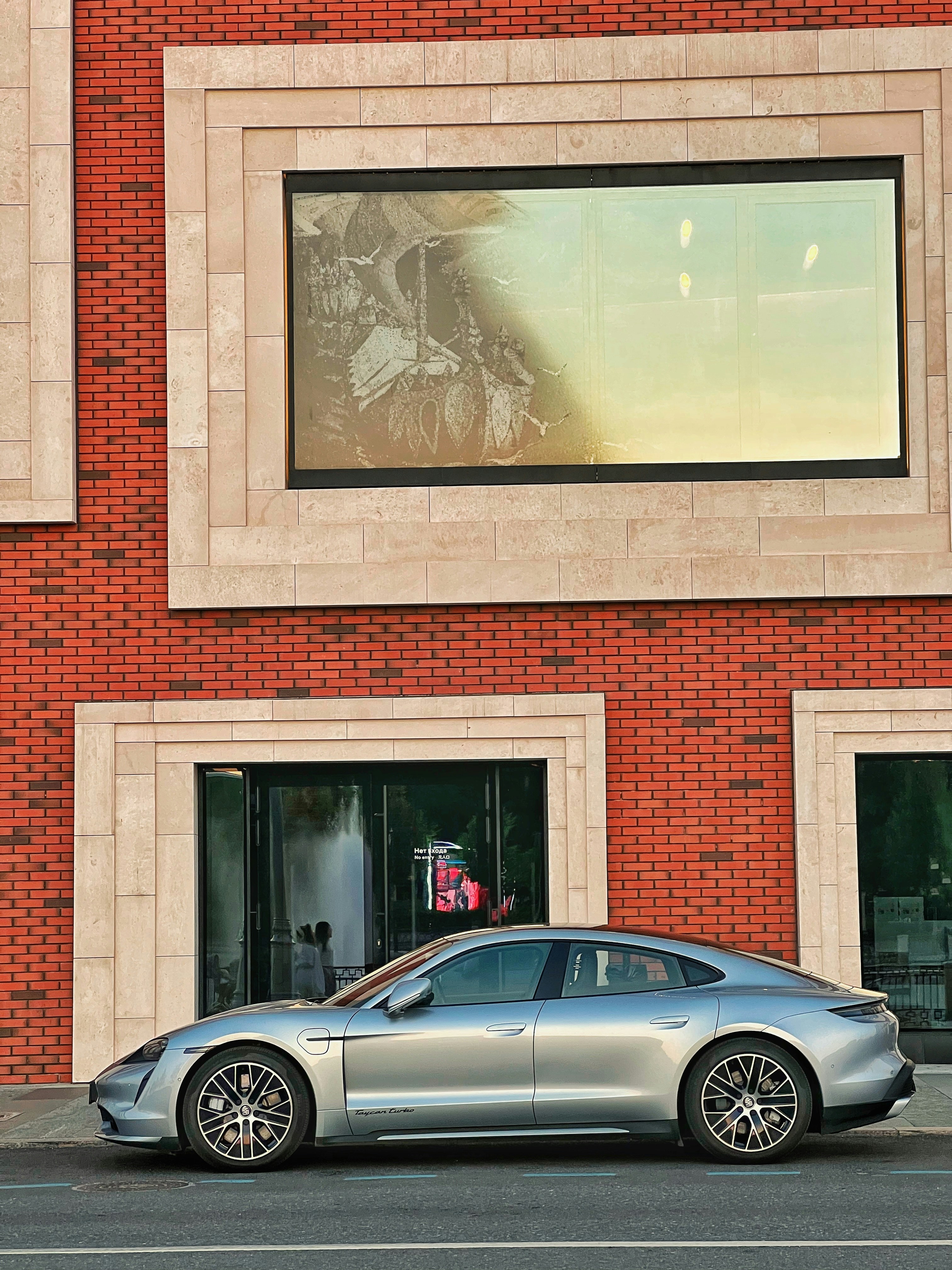 Street photography | Silver luxury sedan parked by a brick building.