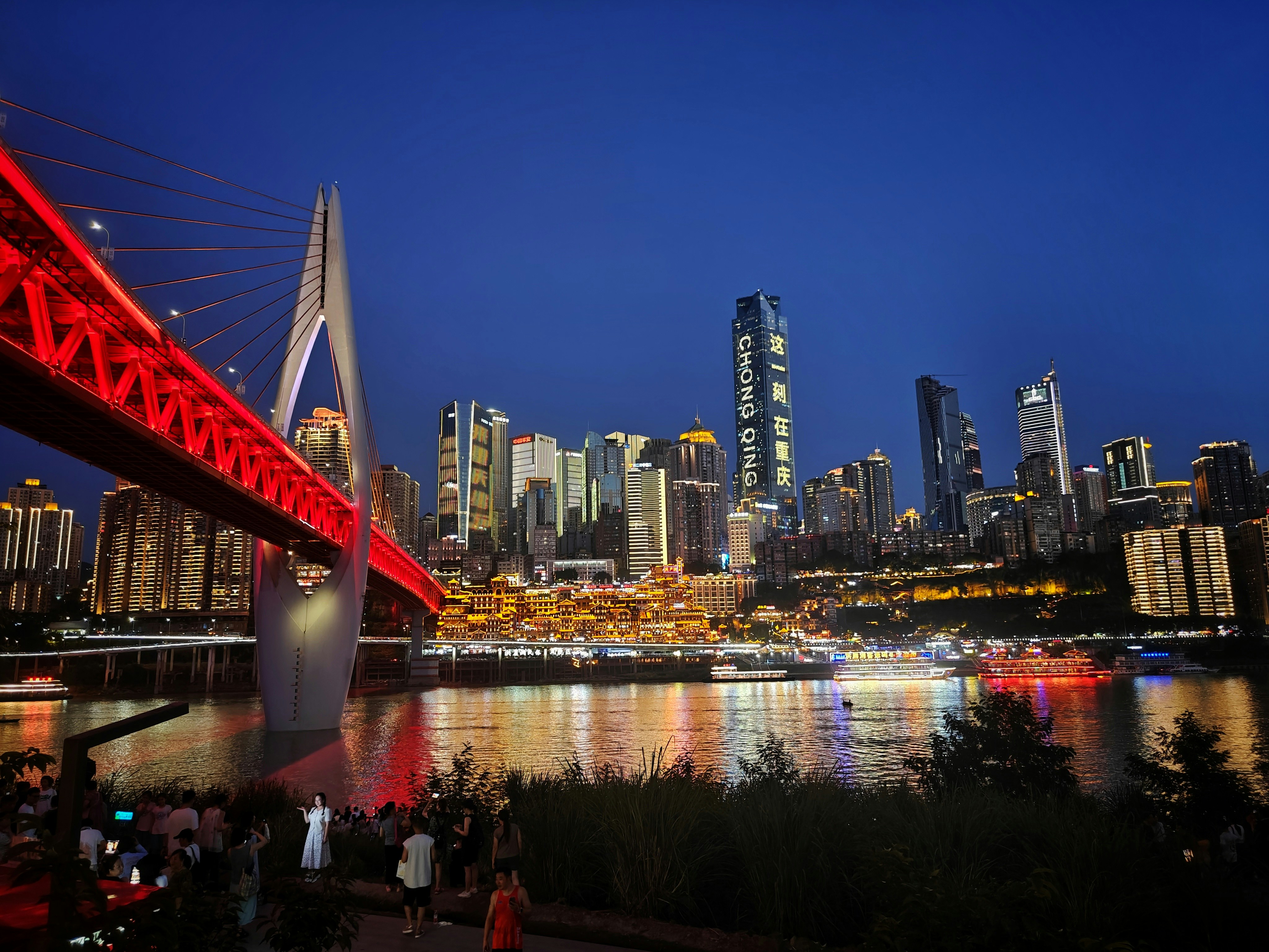 Qiansimen Jialingjiang Bridge and the view towards the Hongyadong Custom Scene Area. | City skyline illuminated at night with a red bridge.