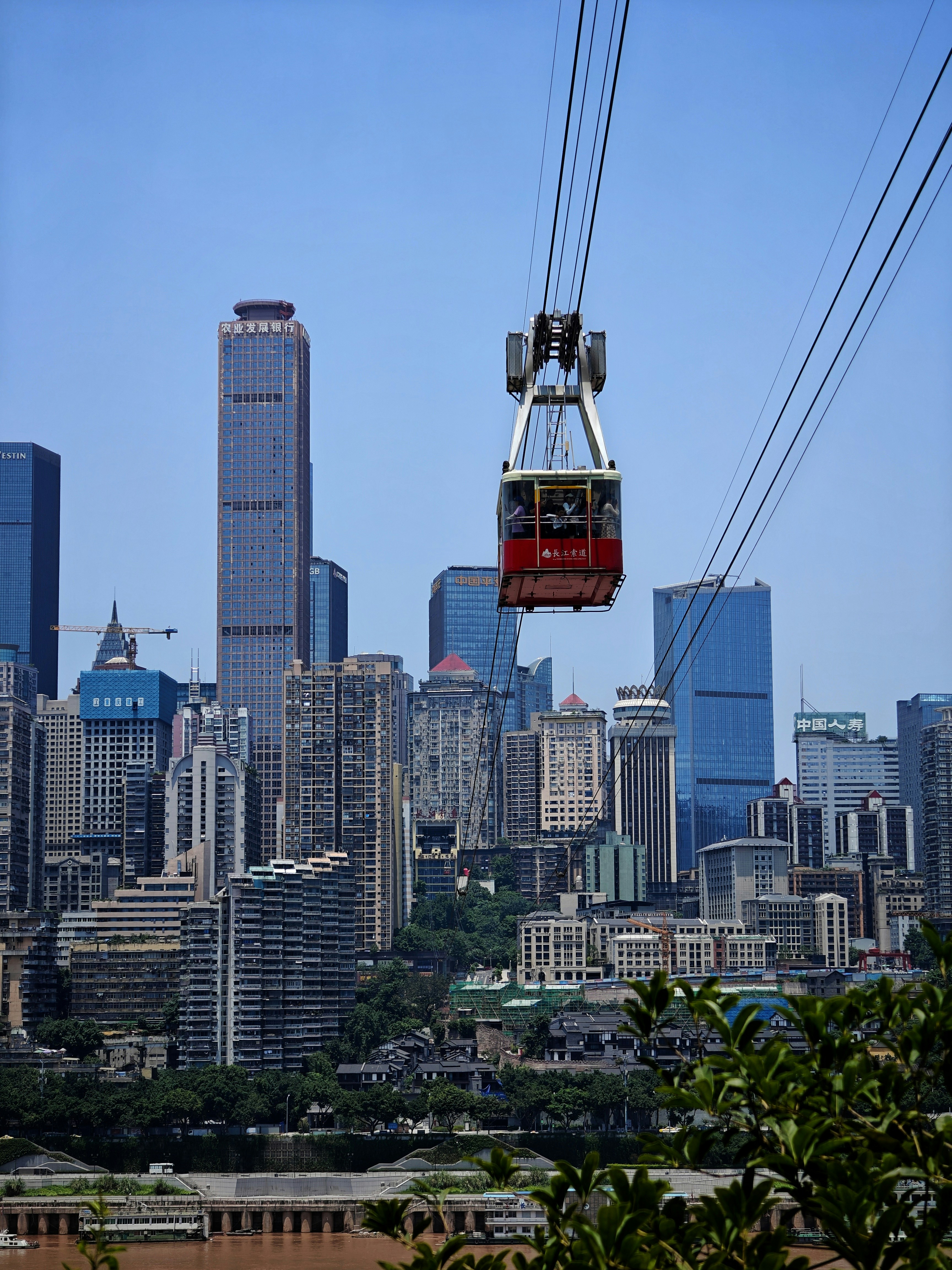 Chongqing Changjiang Cableway over the Changjiang River. | Cable car crosses cityscape with modern skyscrapers