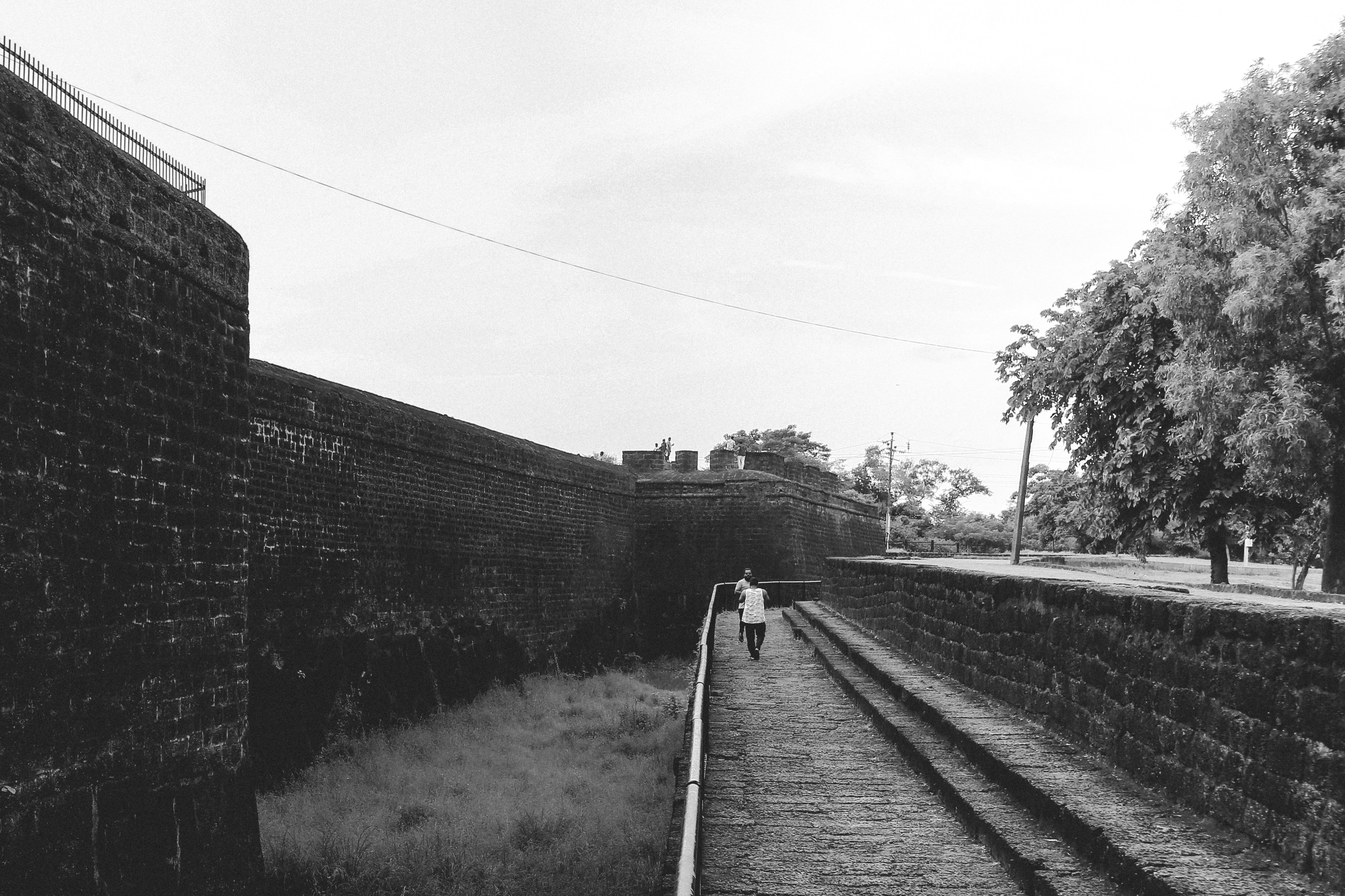 stone walls and pathways of a historic Goan fort showcasing timeless heritage | A person walks on a path beside a stone wall.