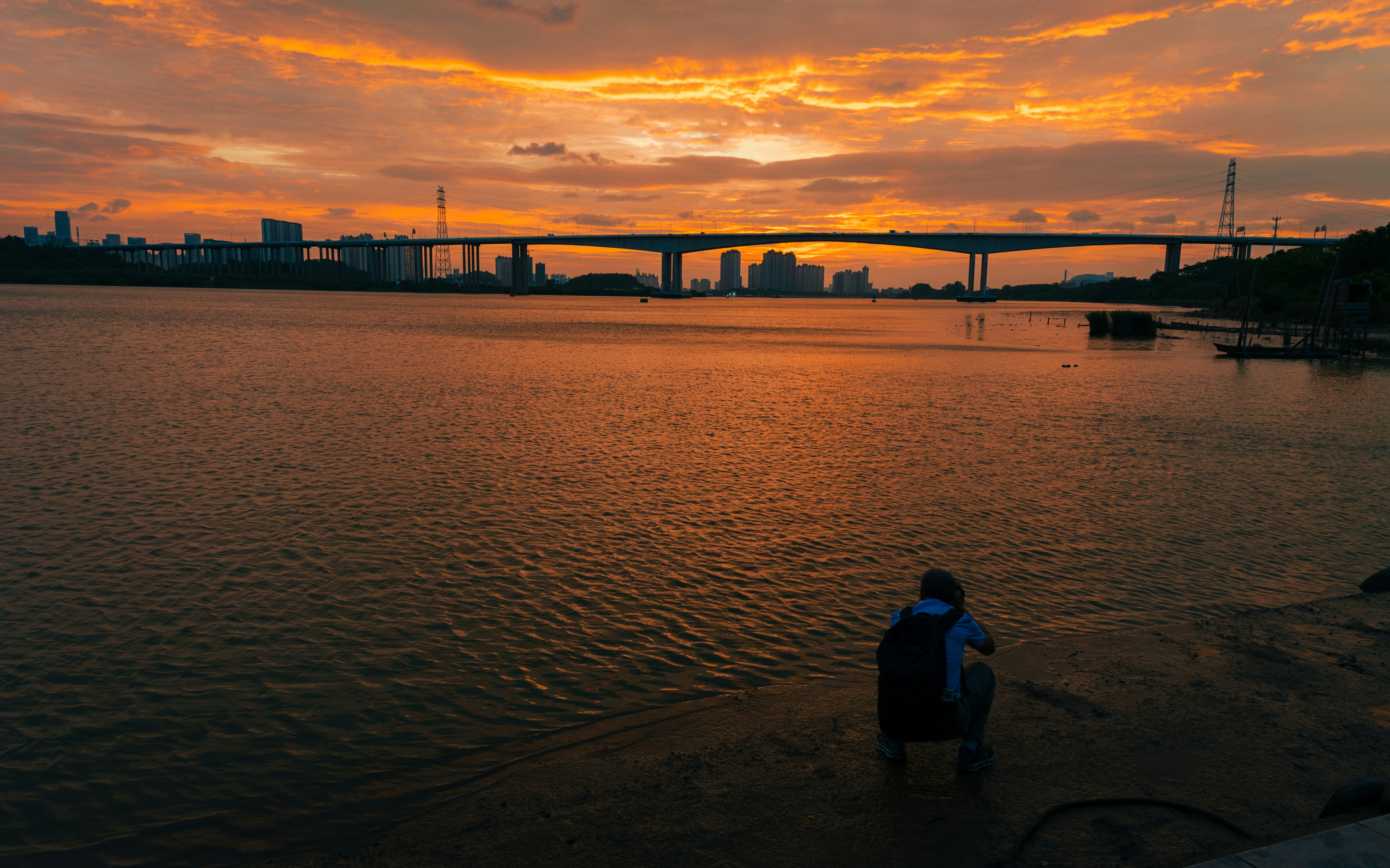 Man watches sunset over river with bridge and city.