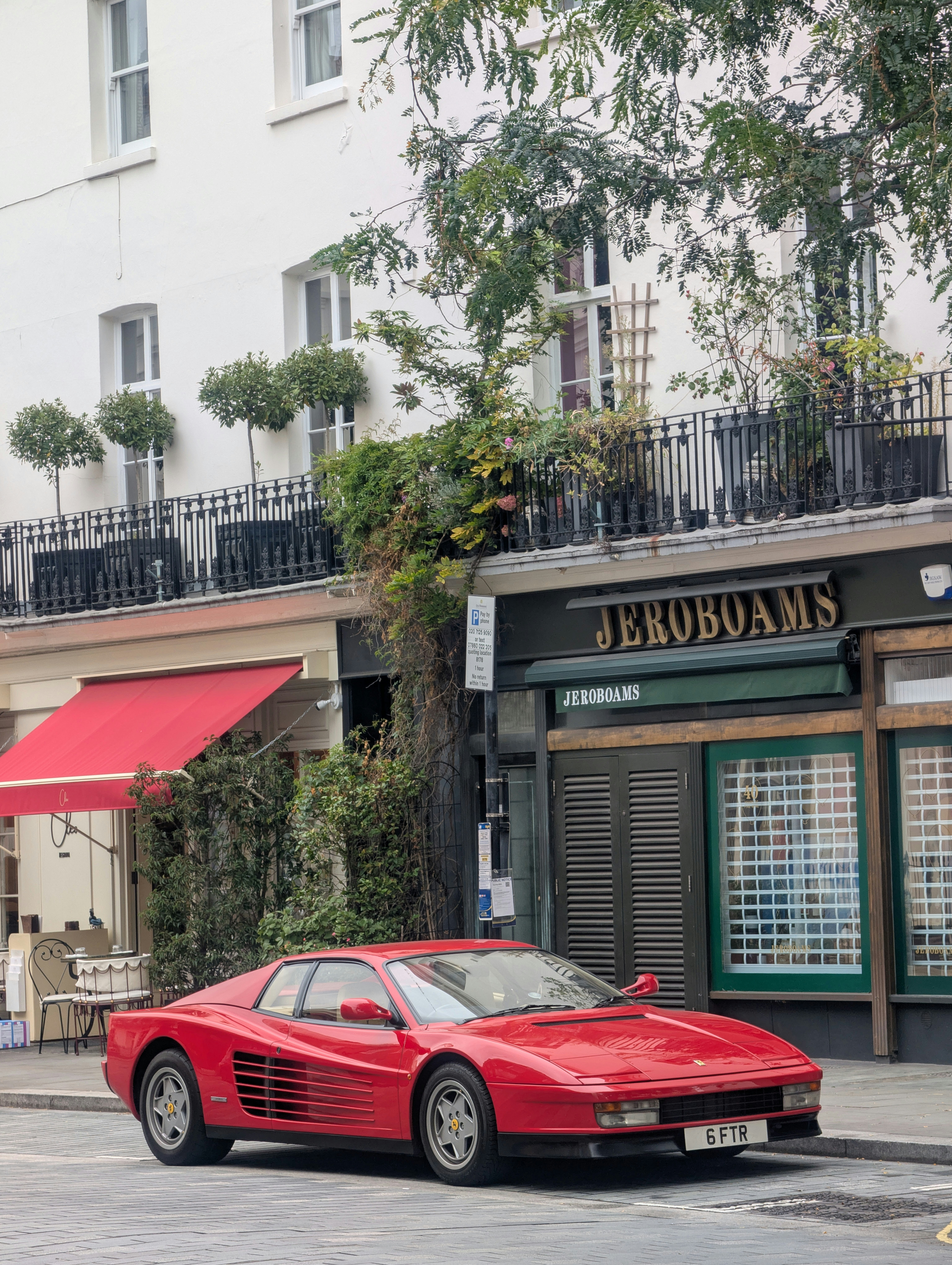 A vibrant red sports car parked on a quaint street, flanked by stylish storefronts and greenery. The scene captures a blend of automotive design and urban architecture.