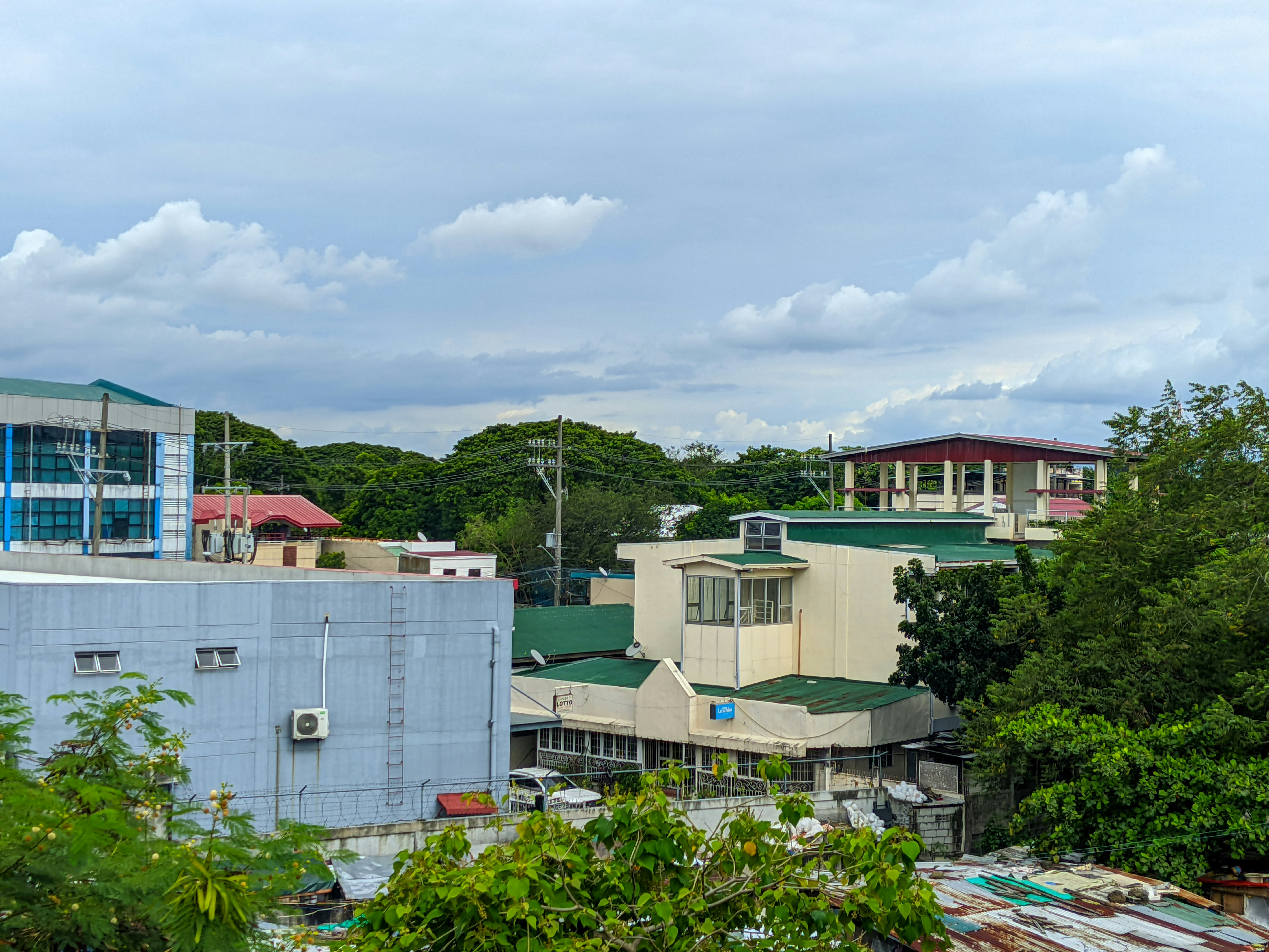 A view of a suburban landscape showcasing a mix of residential and commercial buildings under a cloudy sky. Lush greenery frames the scene.