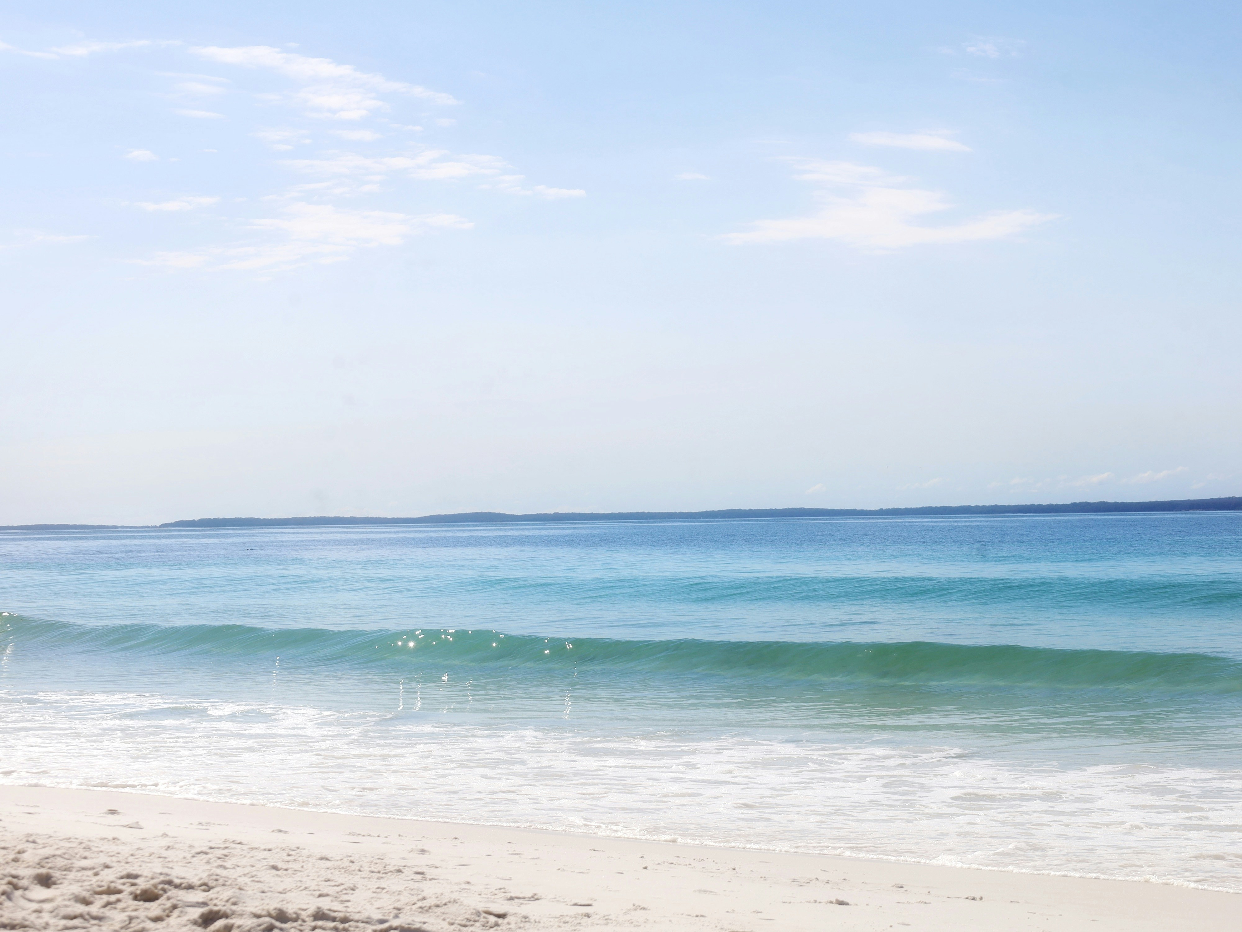 Gentle waves lap a sandy beach under a clear sky.