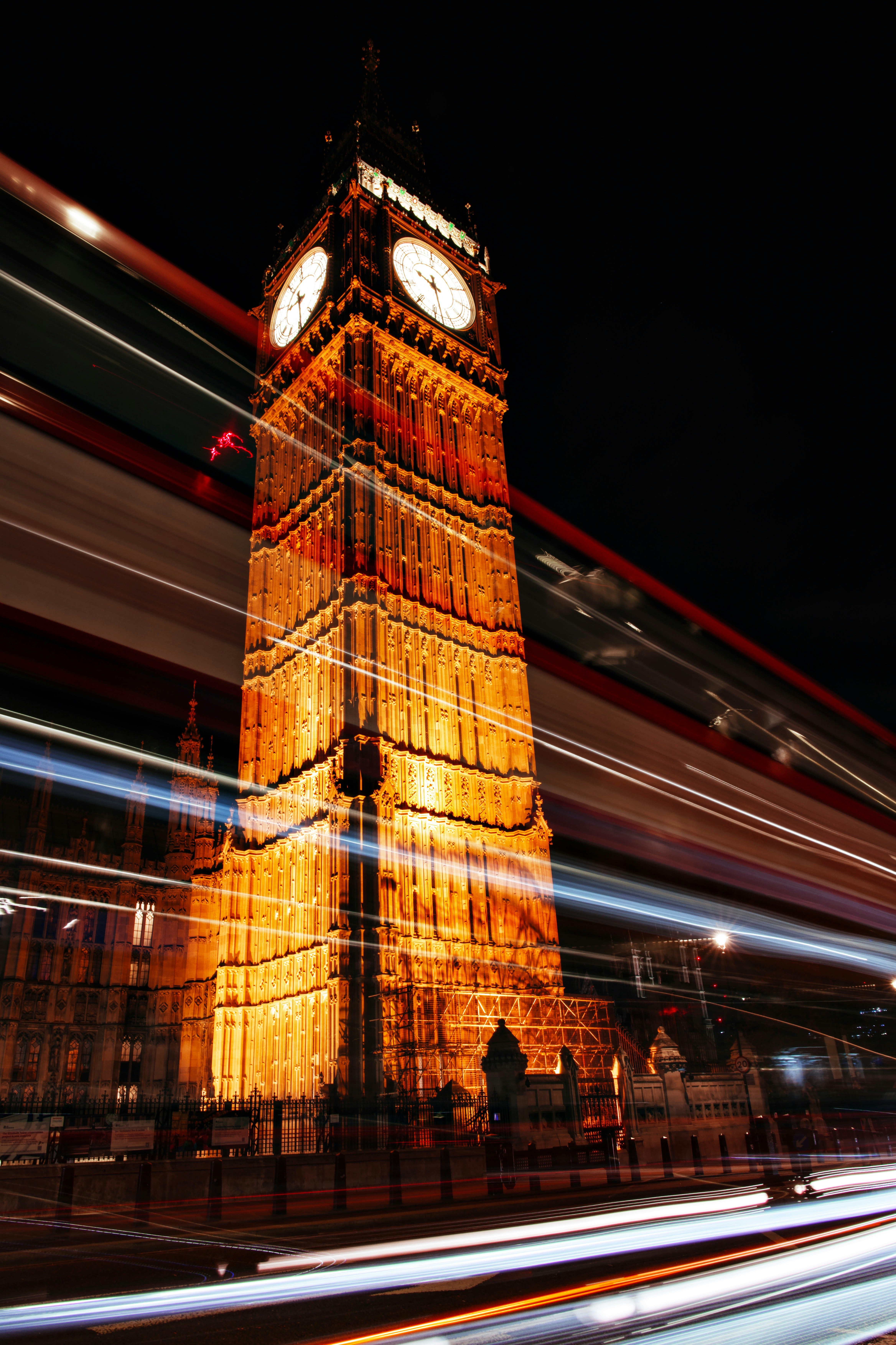 This striking nighttime photo captures the iconic Elizabeth Tower, commonly known as Big Ben, in London. The tower is beautifully illuminated against the dark sky, while the long exposure creates dynamic light trails from passing vehicles, adding a sense of motion and energy to the scene. | Big ben illuminated at night with light trails