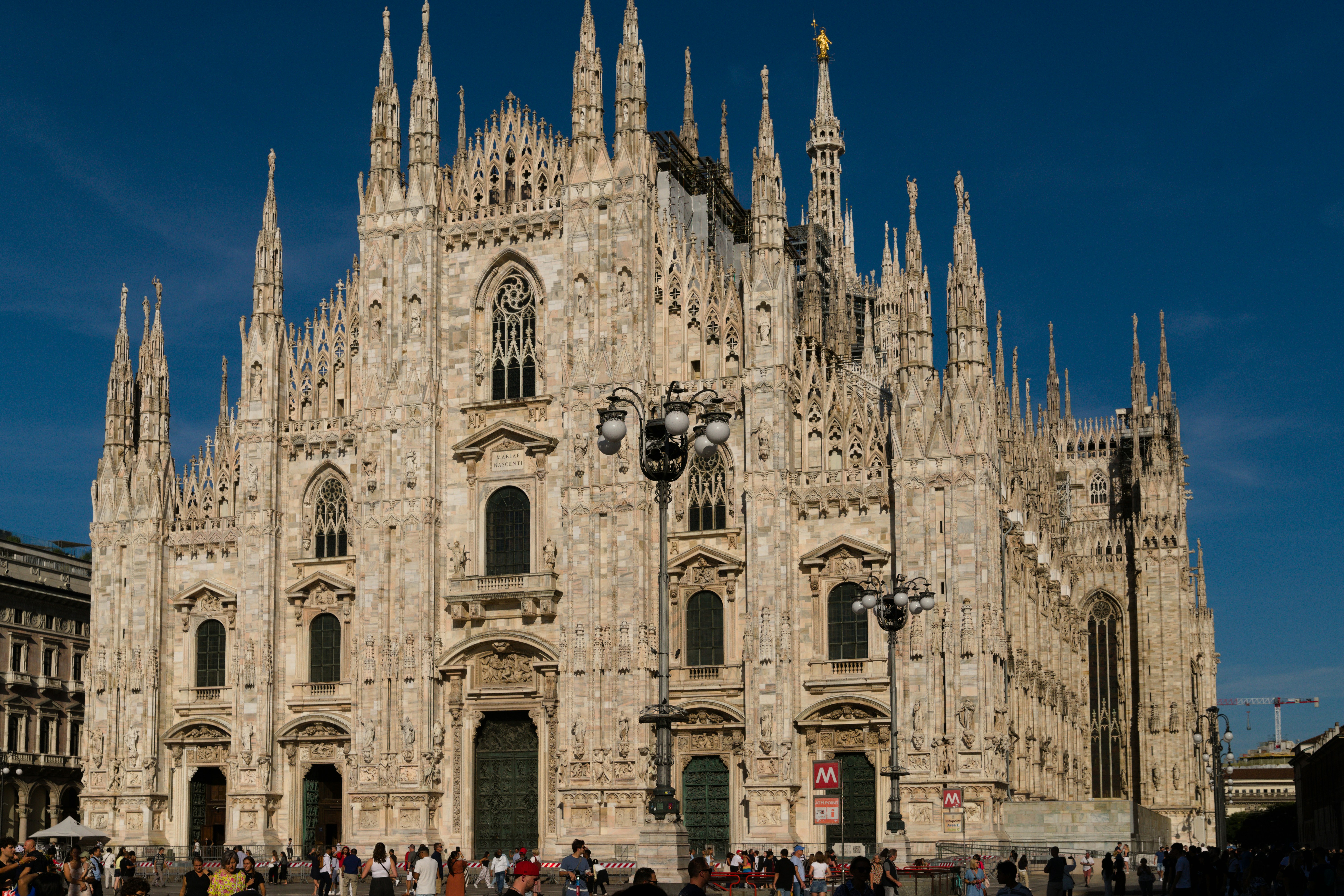 Intricate Gothic architecture of the Milan Cathedral, showcasing its spires and detailed façade against a clear blue sky.