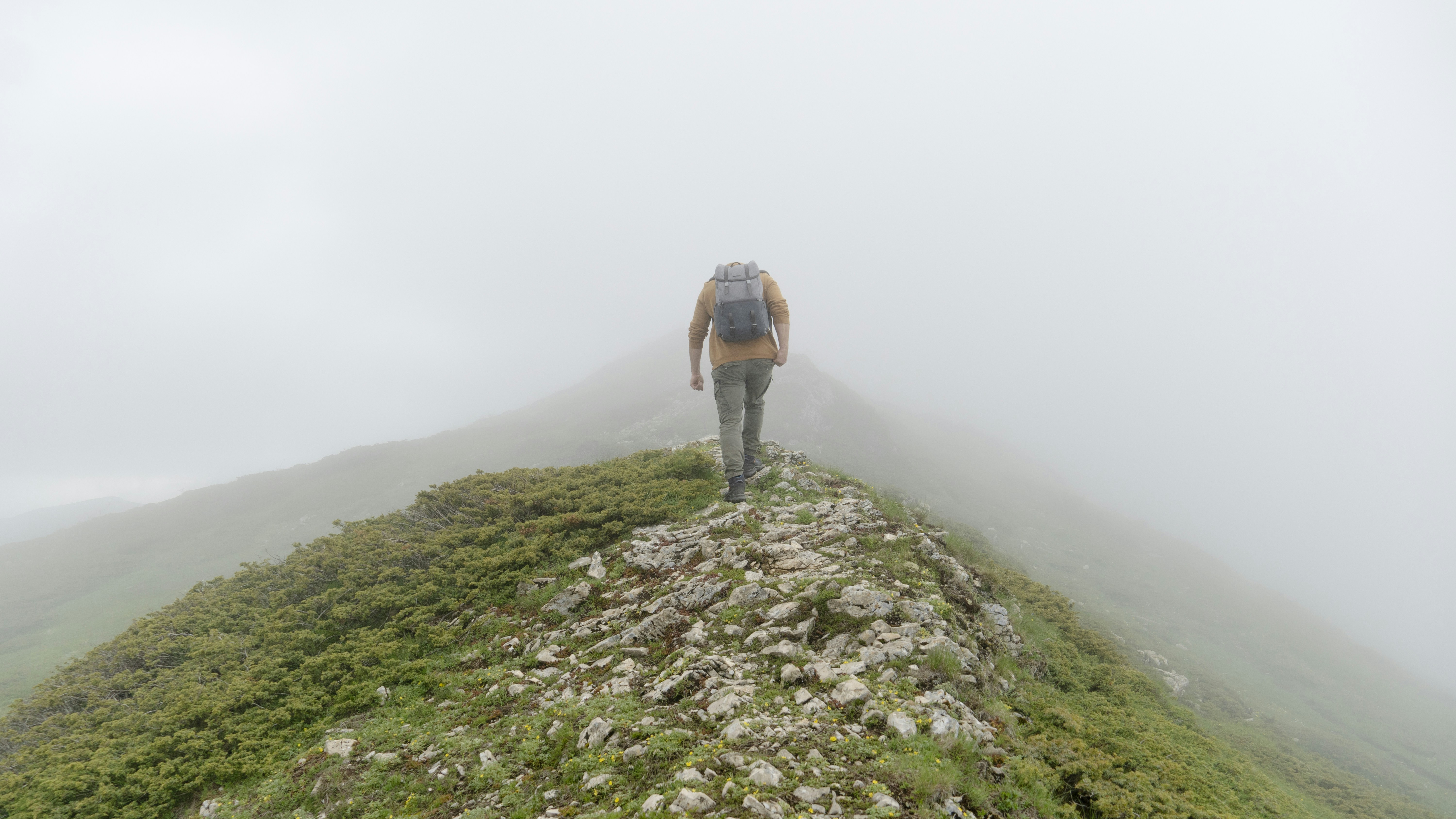 Hiker walks on a rocky mountain ridge in fog.