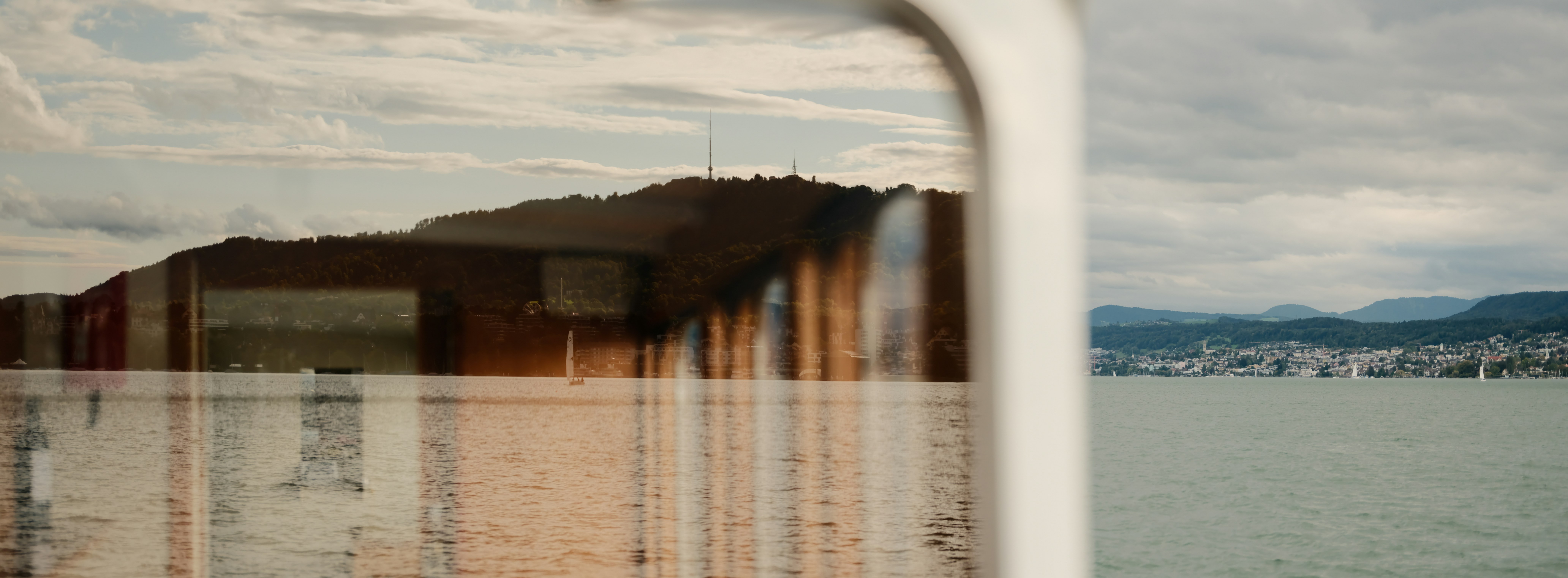 Serene lake view reflecting distant hills and a cloudy sky, framed by a window's edge.