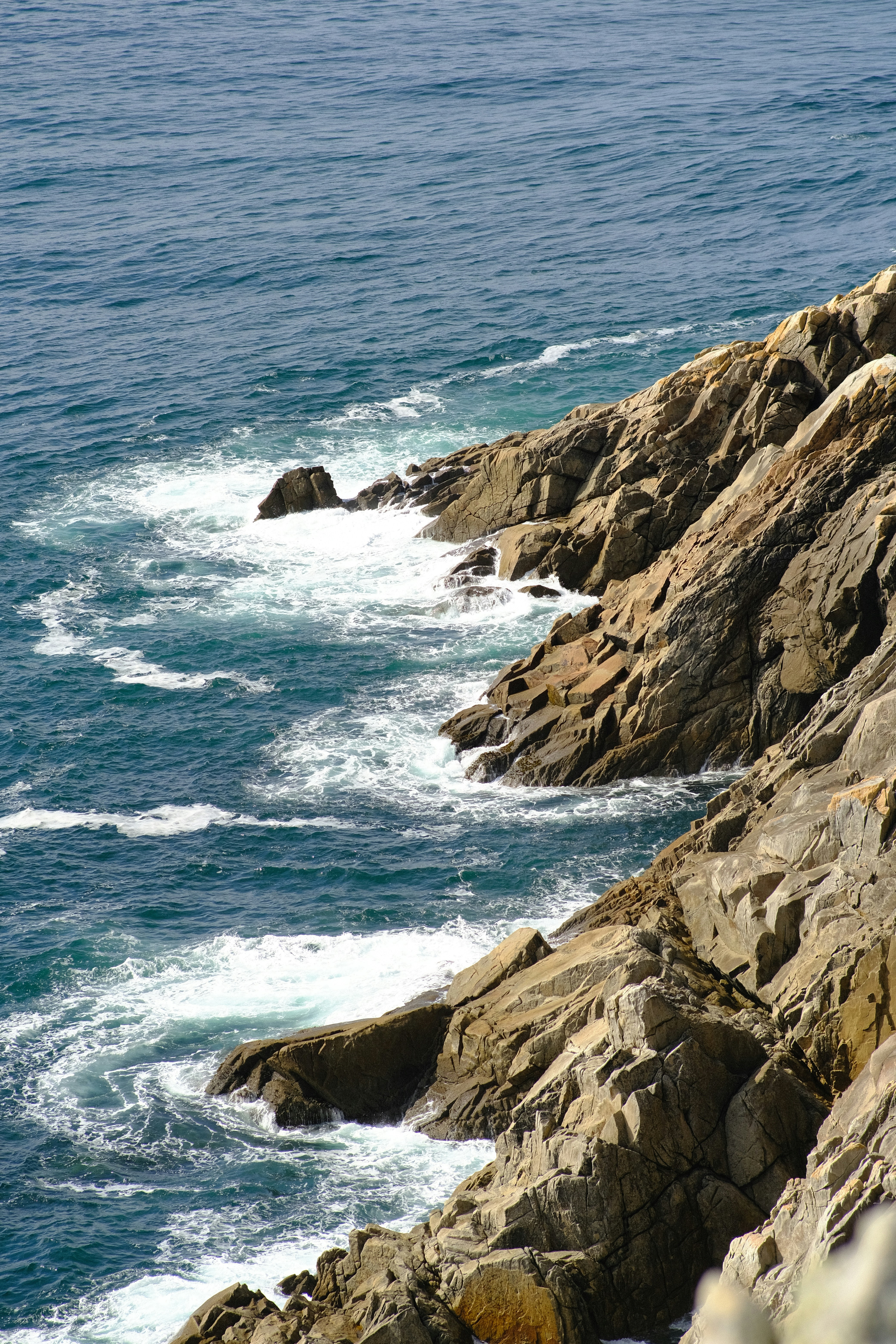 Waves crash against a rocky coastline under blue sky.
