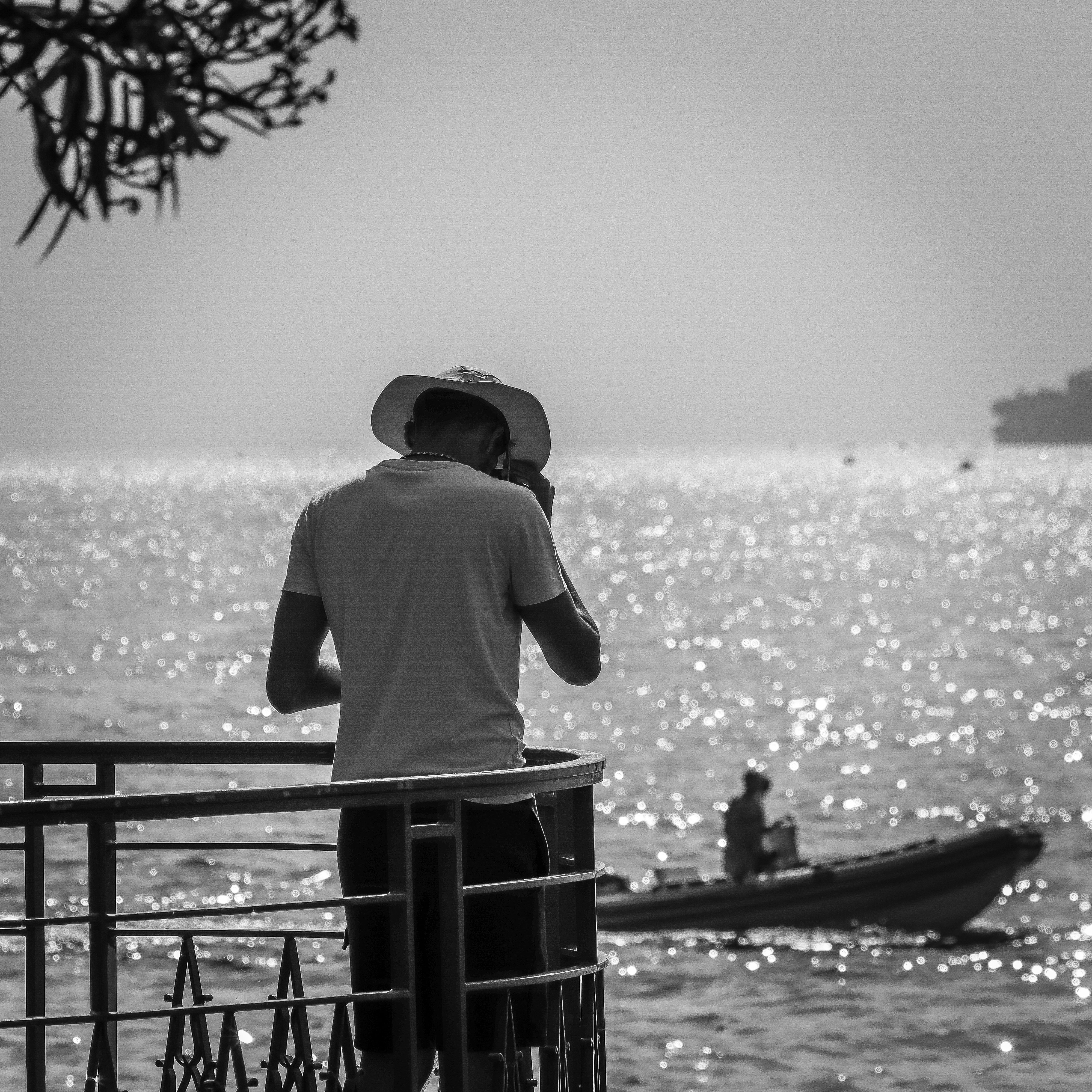 Man with hat photographs sparkling ocean with boat.