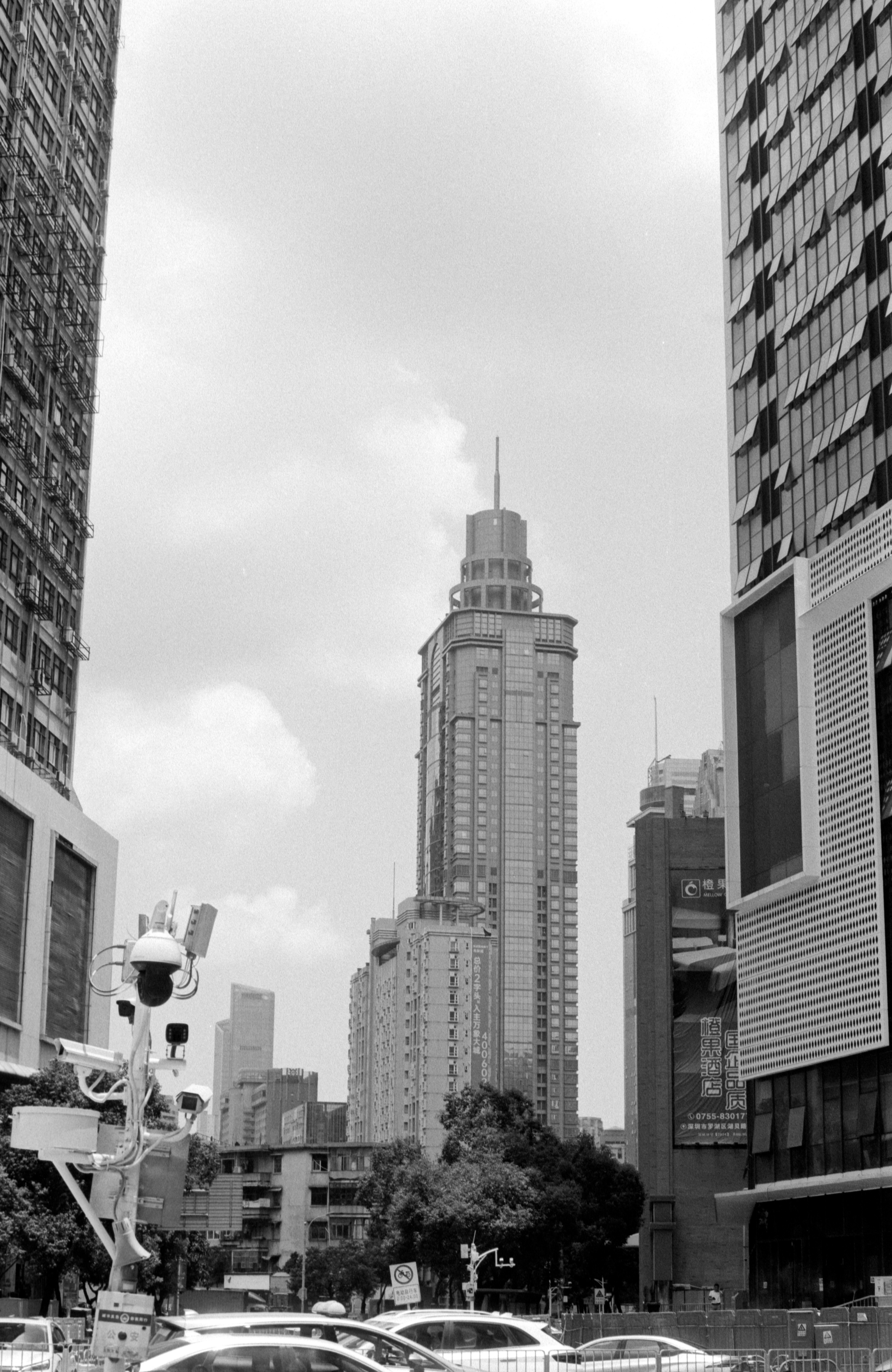 A towering skyscraper rises above the cityscape, flanked by modern buildings and bustling traffic below. The monochrome tones emphasize the architectural contrasts.