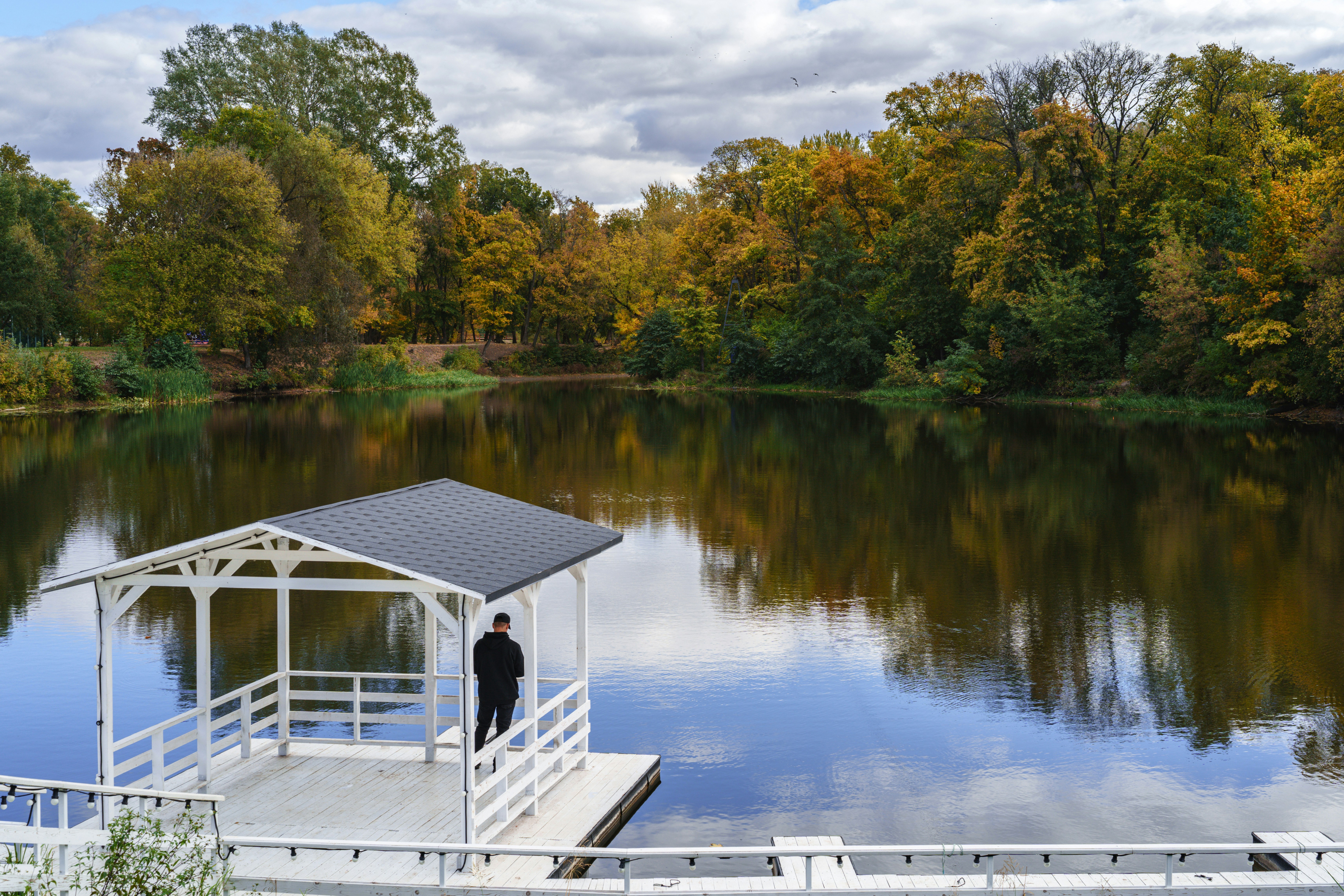 Man standing on a white gazebo by a lake.