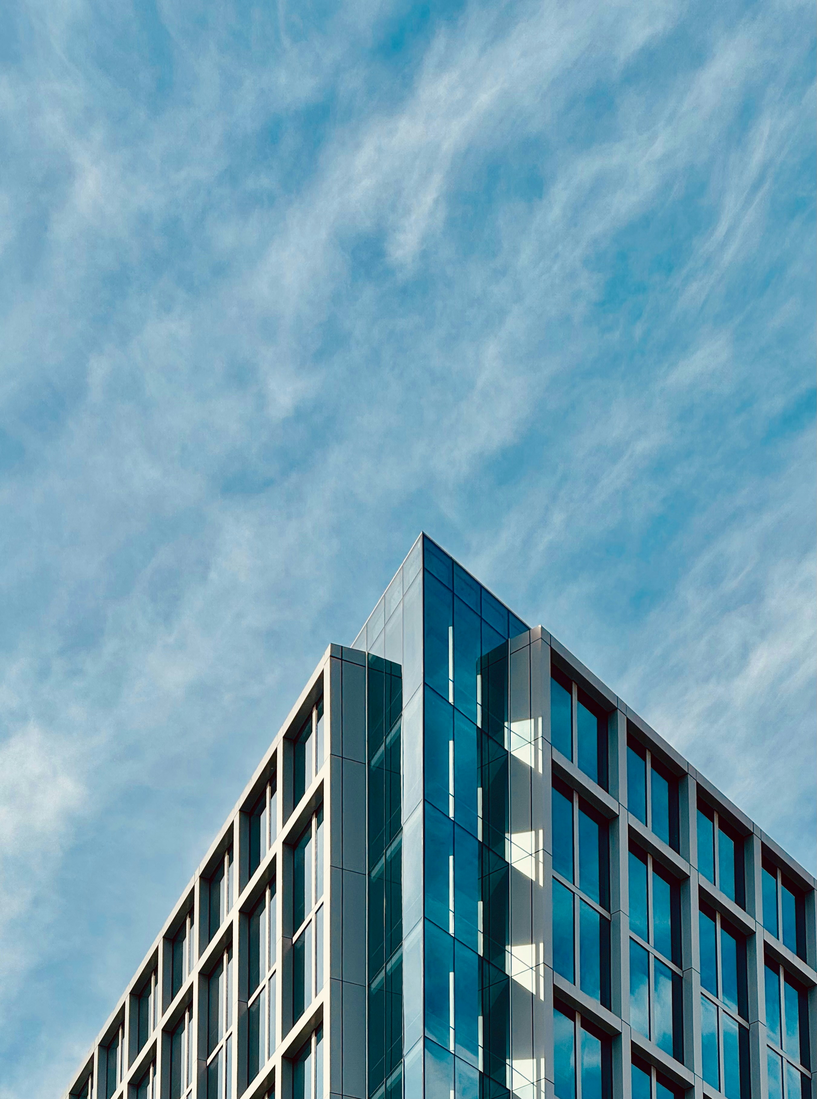 Angular glass facade of a contemporary building under a blue sky with wispy clouds.