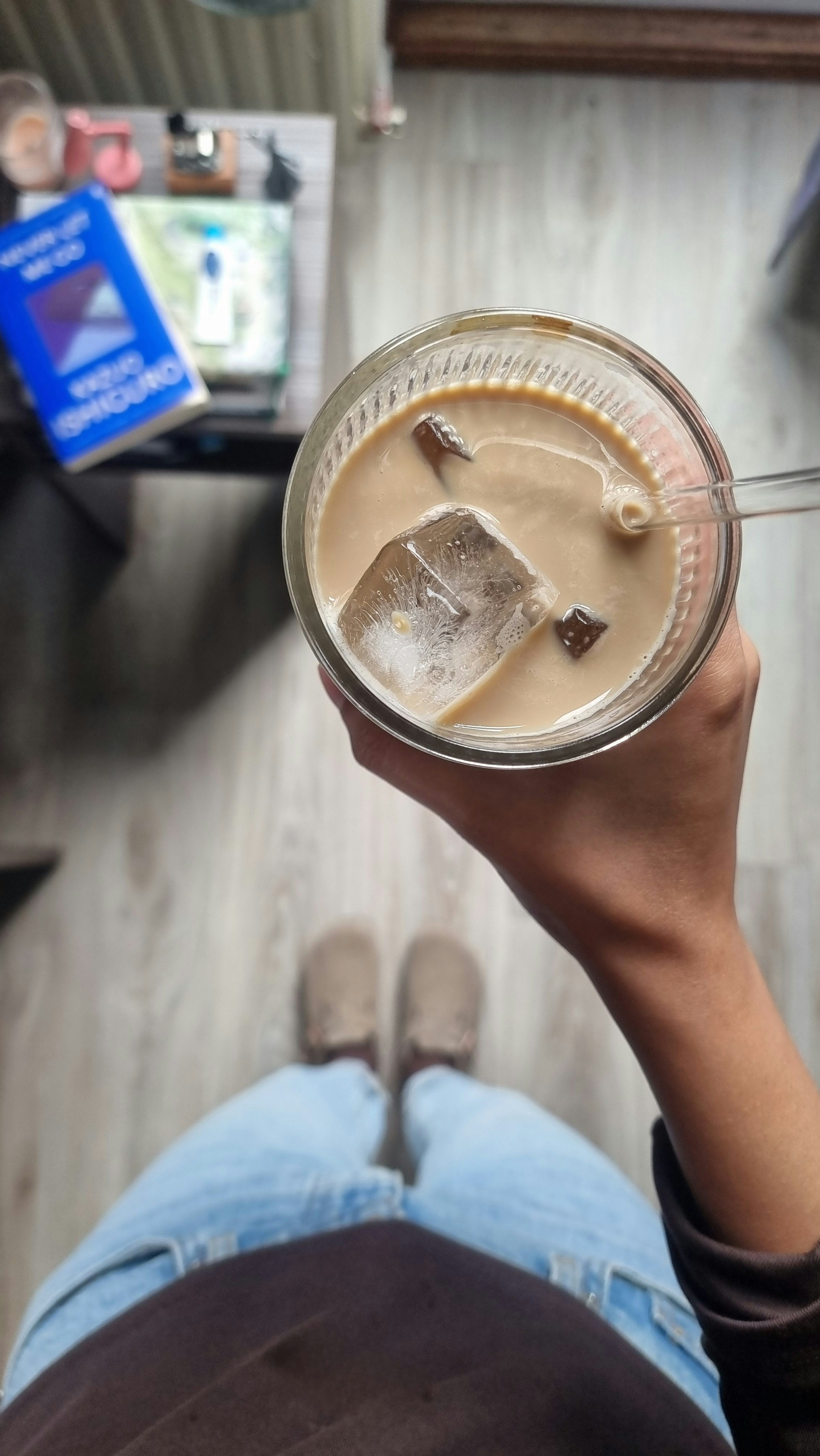 Hand holding iced coffee with ice cubes and straw.