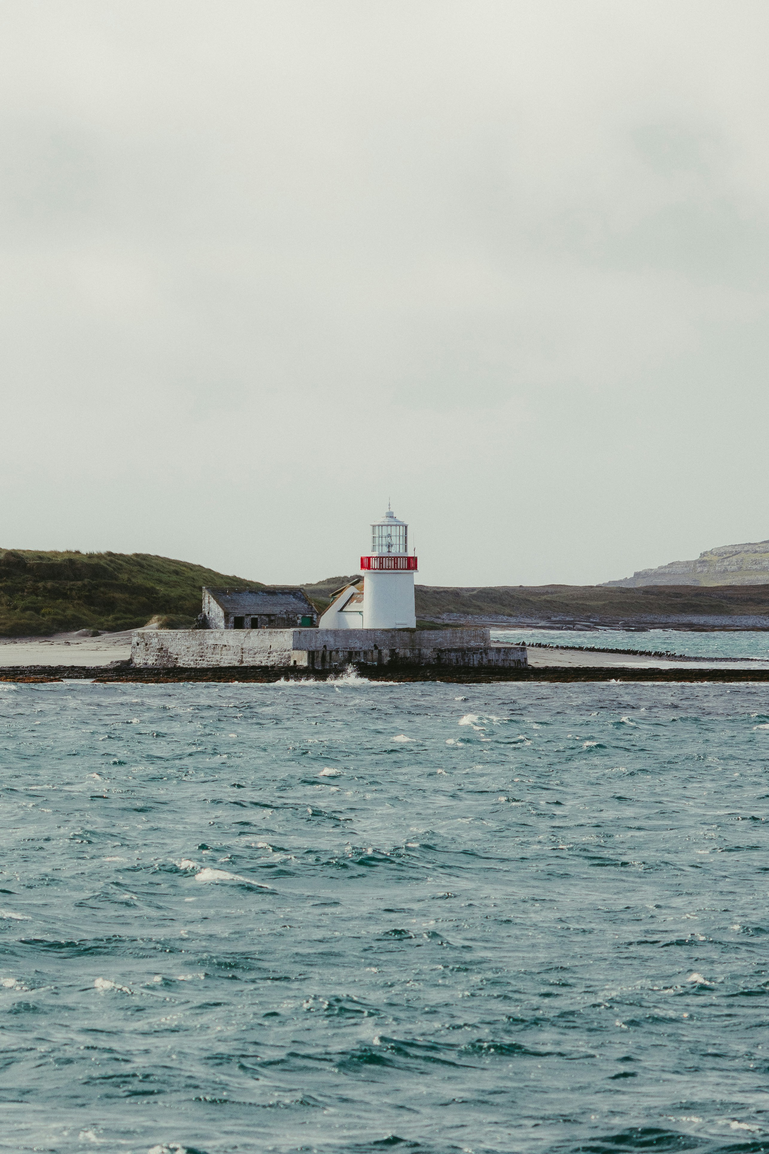 White lighthouse on a rocky island with choppy seas.