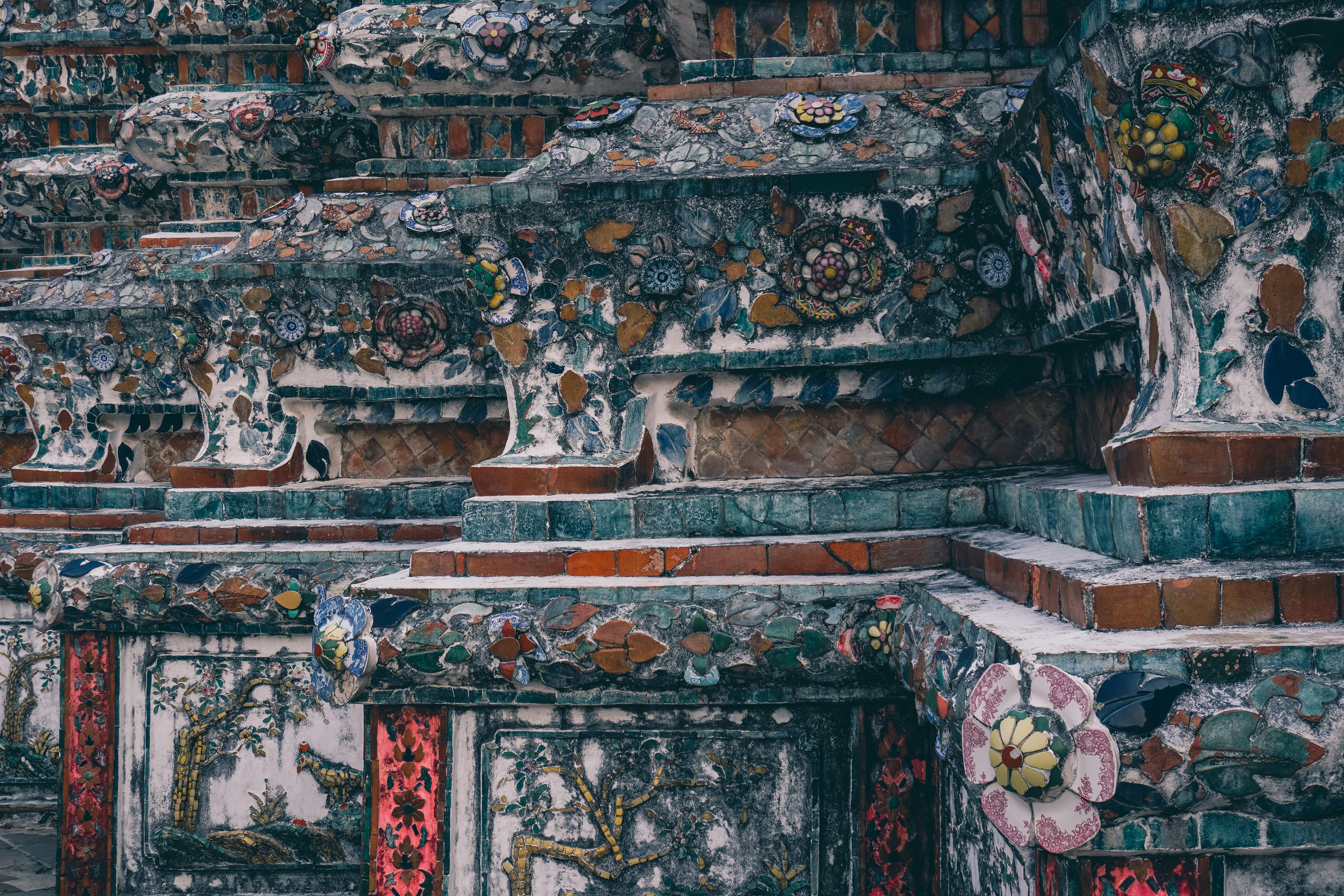 Intricate architectural details of Wat Arun in Bangkok, Thailand — colorful floral mosaics and hand-crafted temple ornaments reflecting traditional Thai art. | Intricate details on a weathered temple facade