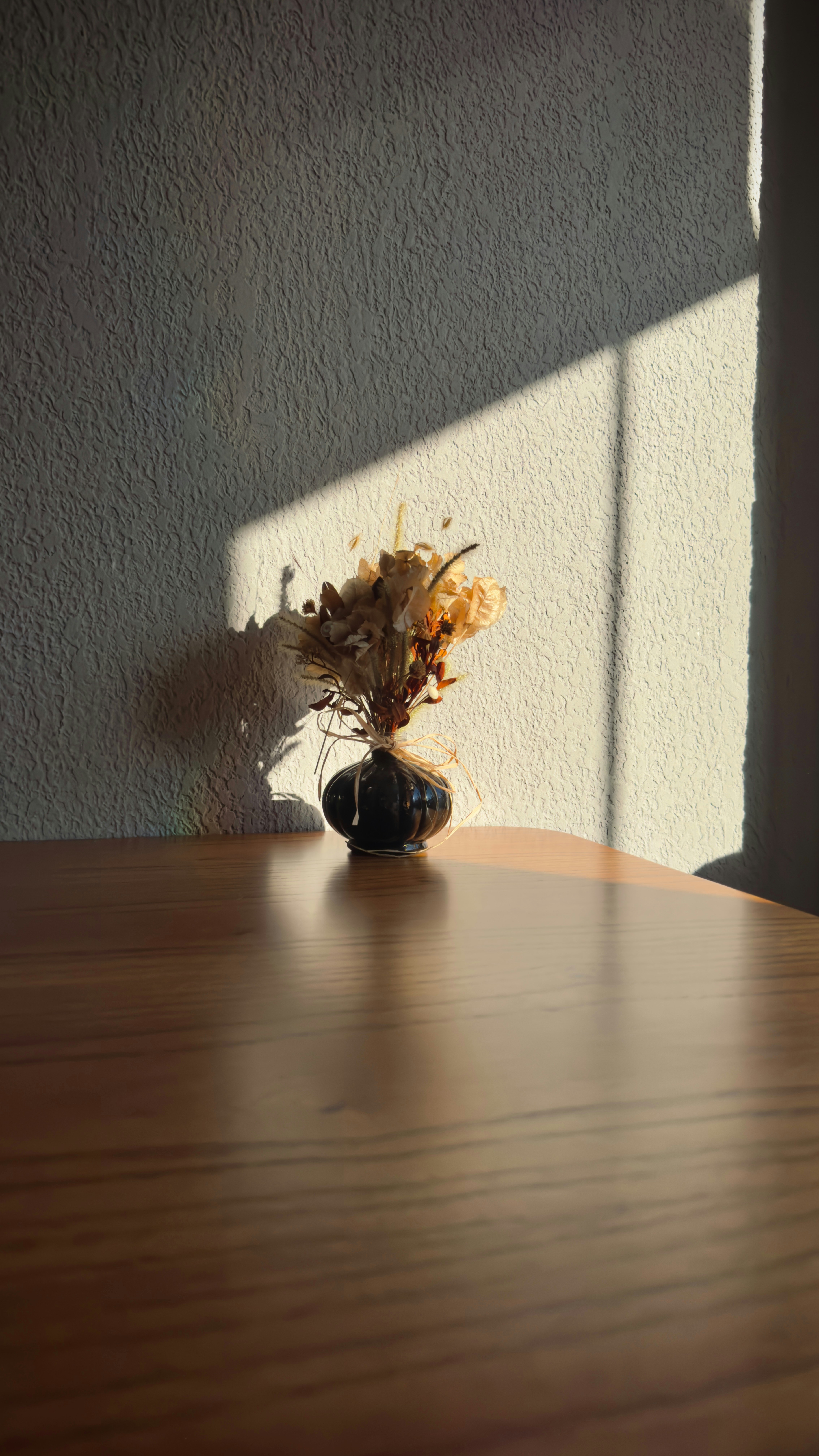 Dried flowers in a dark vase on a wooden table.