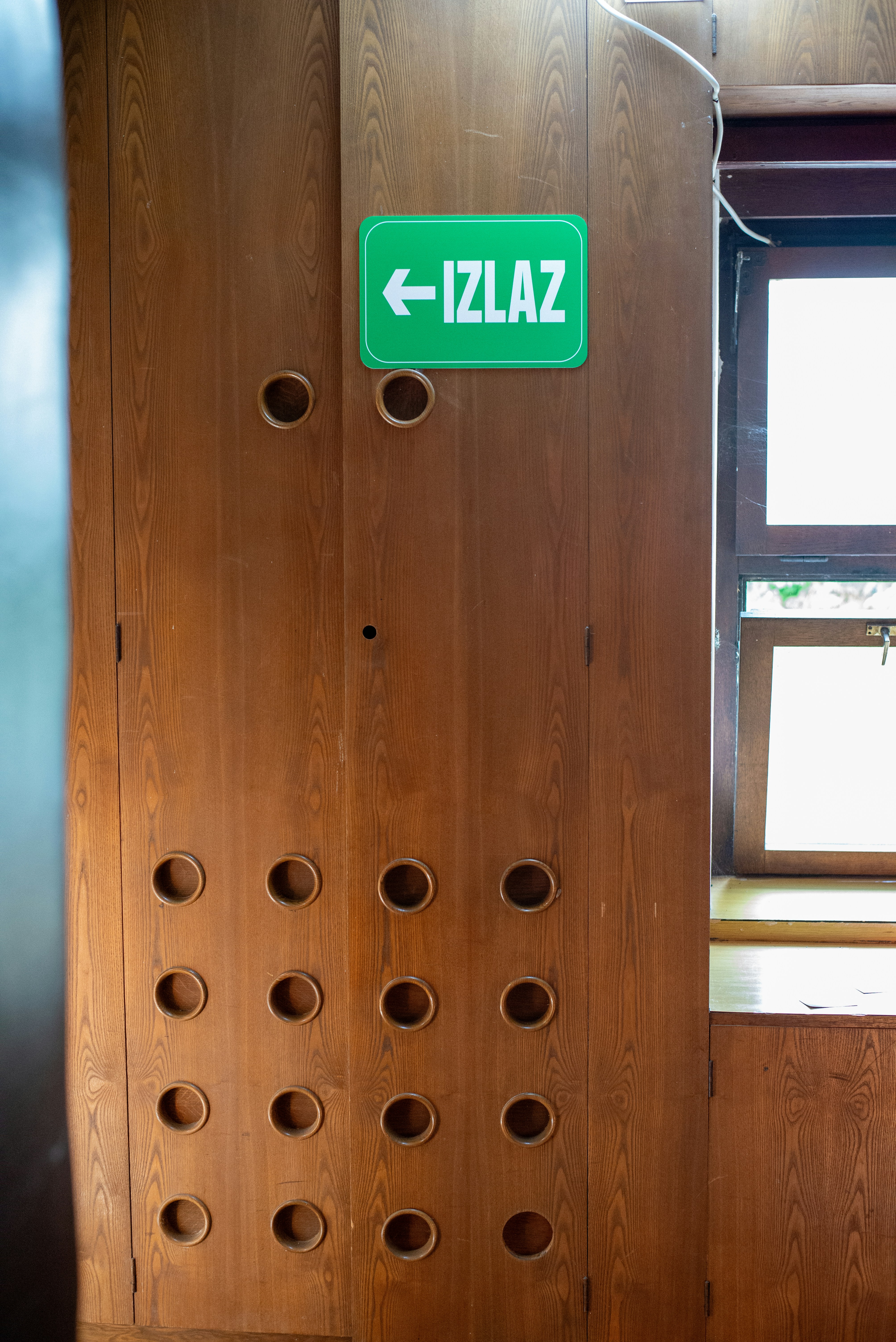 Wooden wall with circular holes and exit sign.