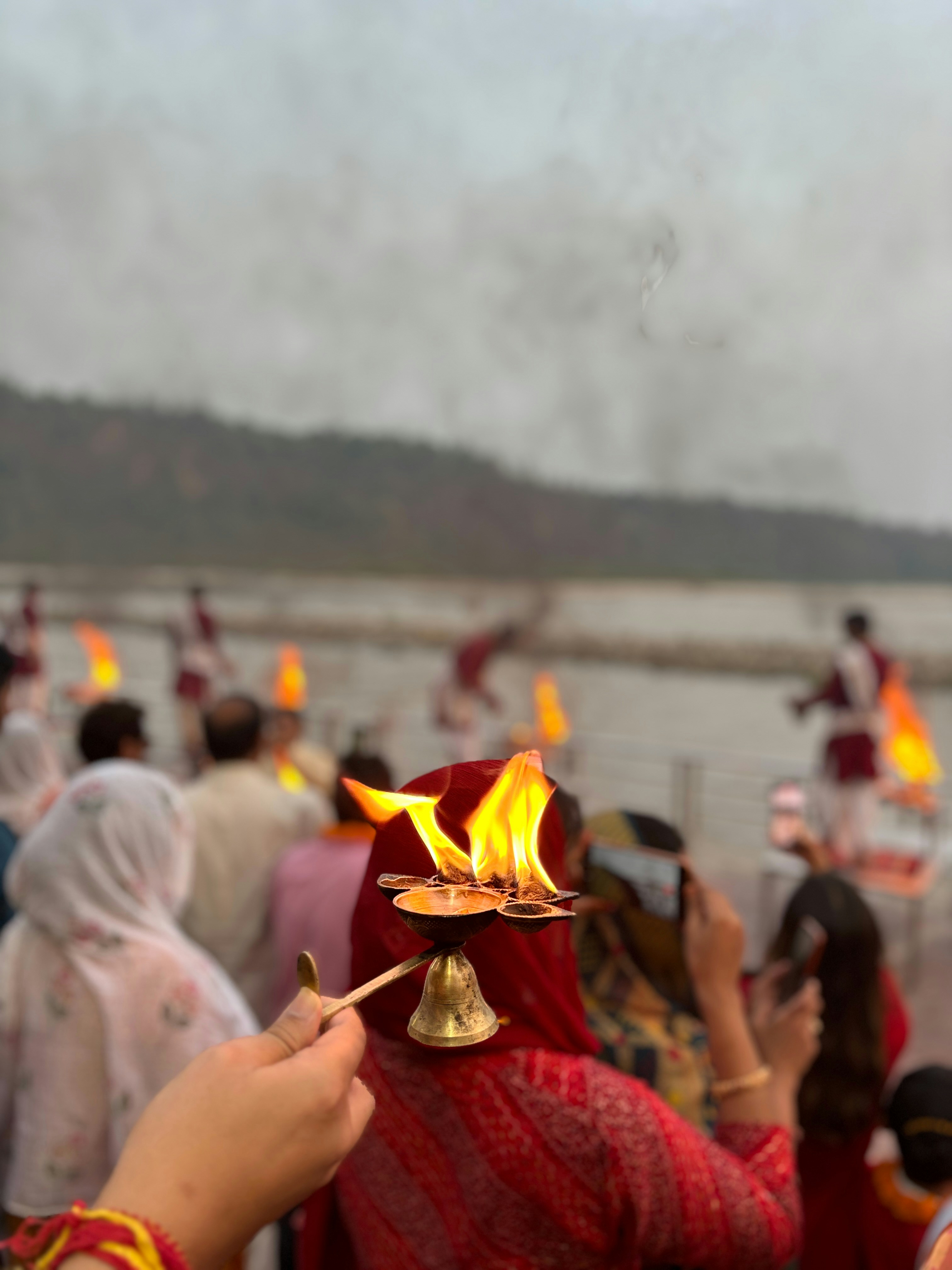 People holding lit lamps by a river at dusk.