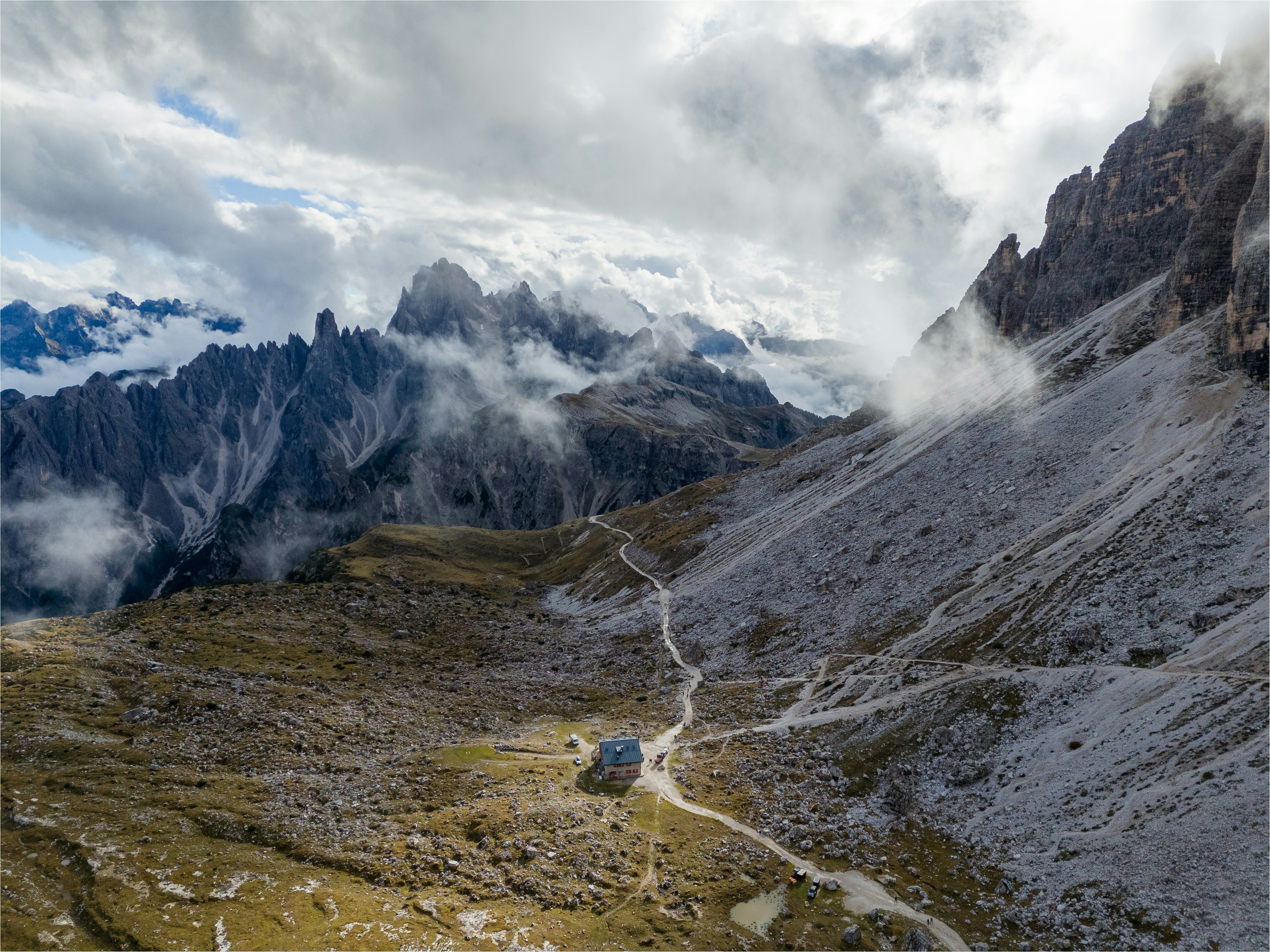 Mountain path leads to small building in cloudy landscape