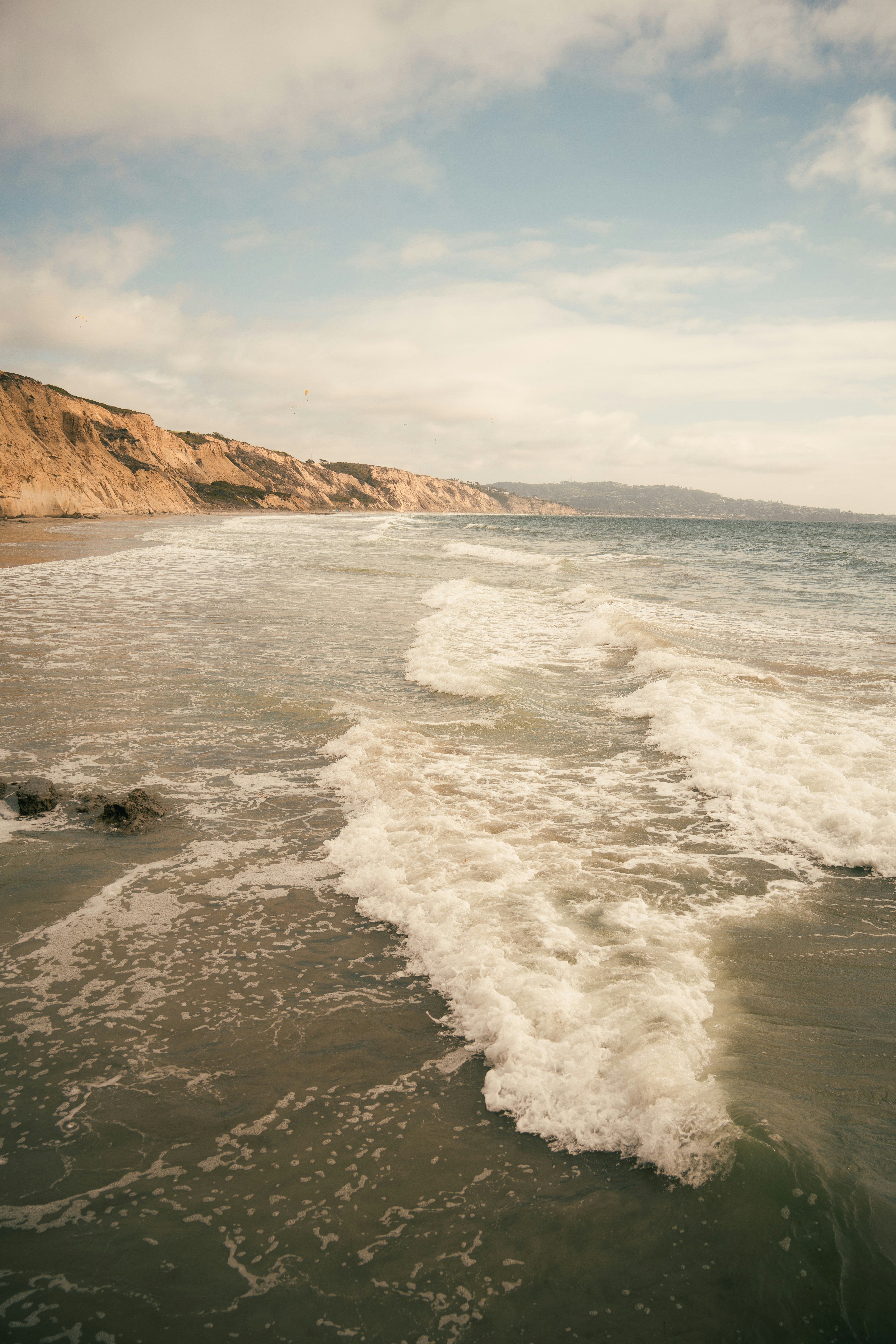 Waves crash on a sandy beach with cliffs.