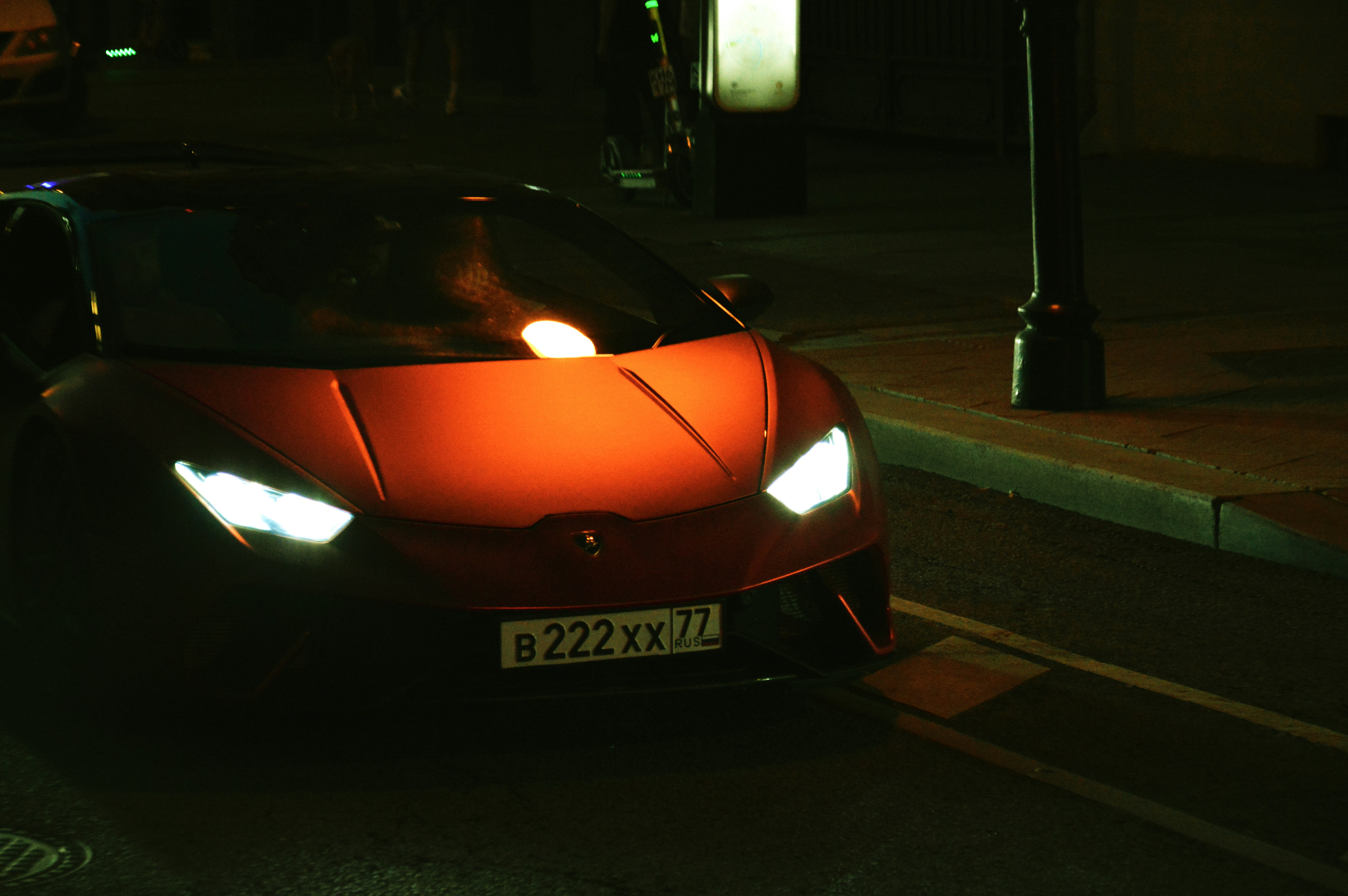 Red sports car driving on a city street at night.