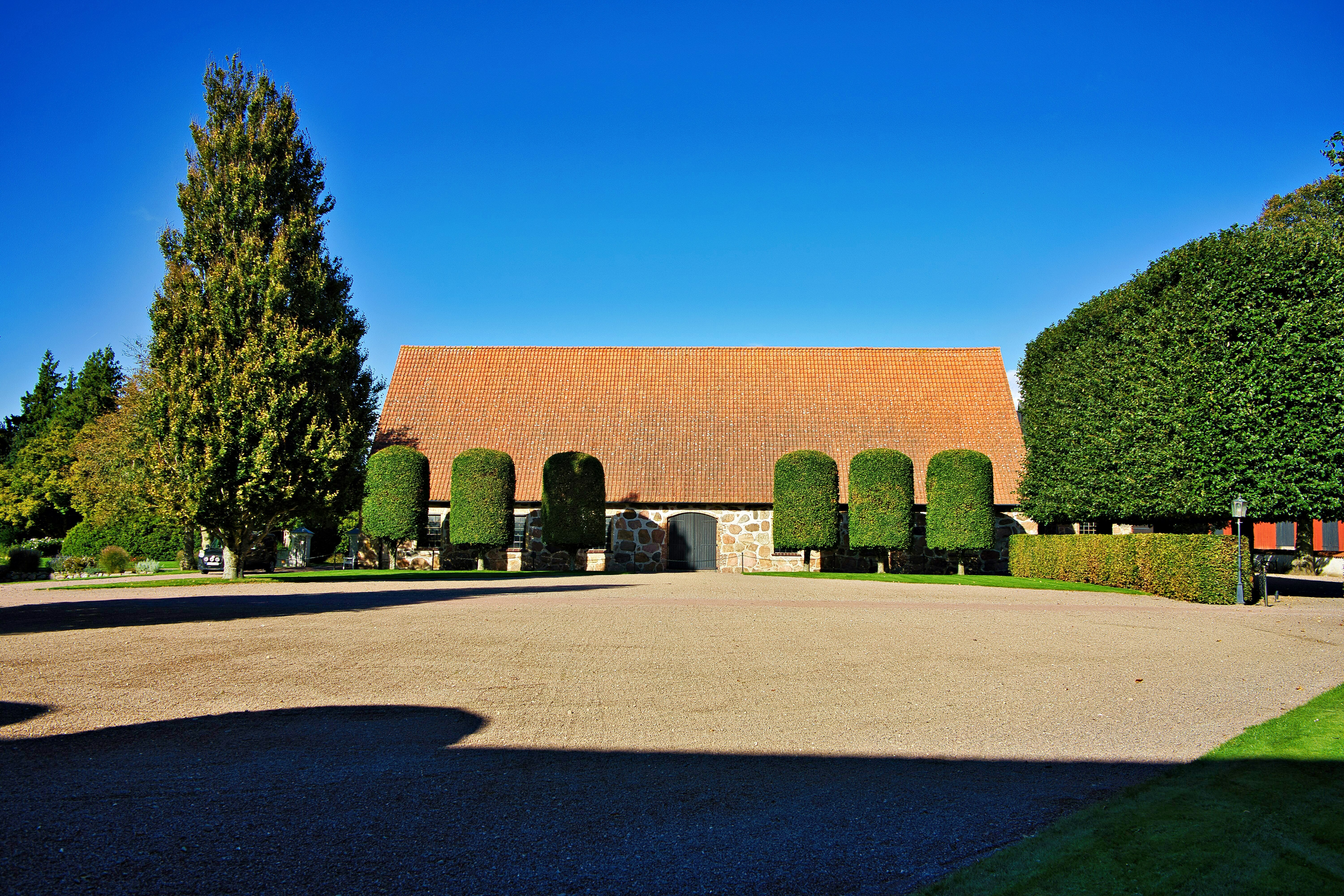 Square and stable building belonging to Krapperups Castle | Barn with manicured trees under a clear blue sky